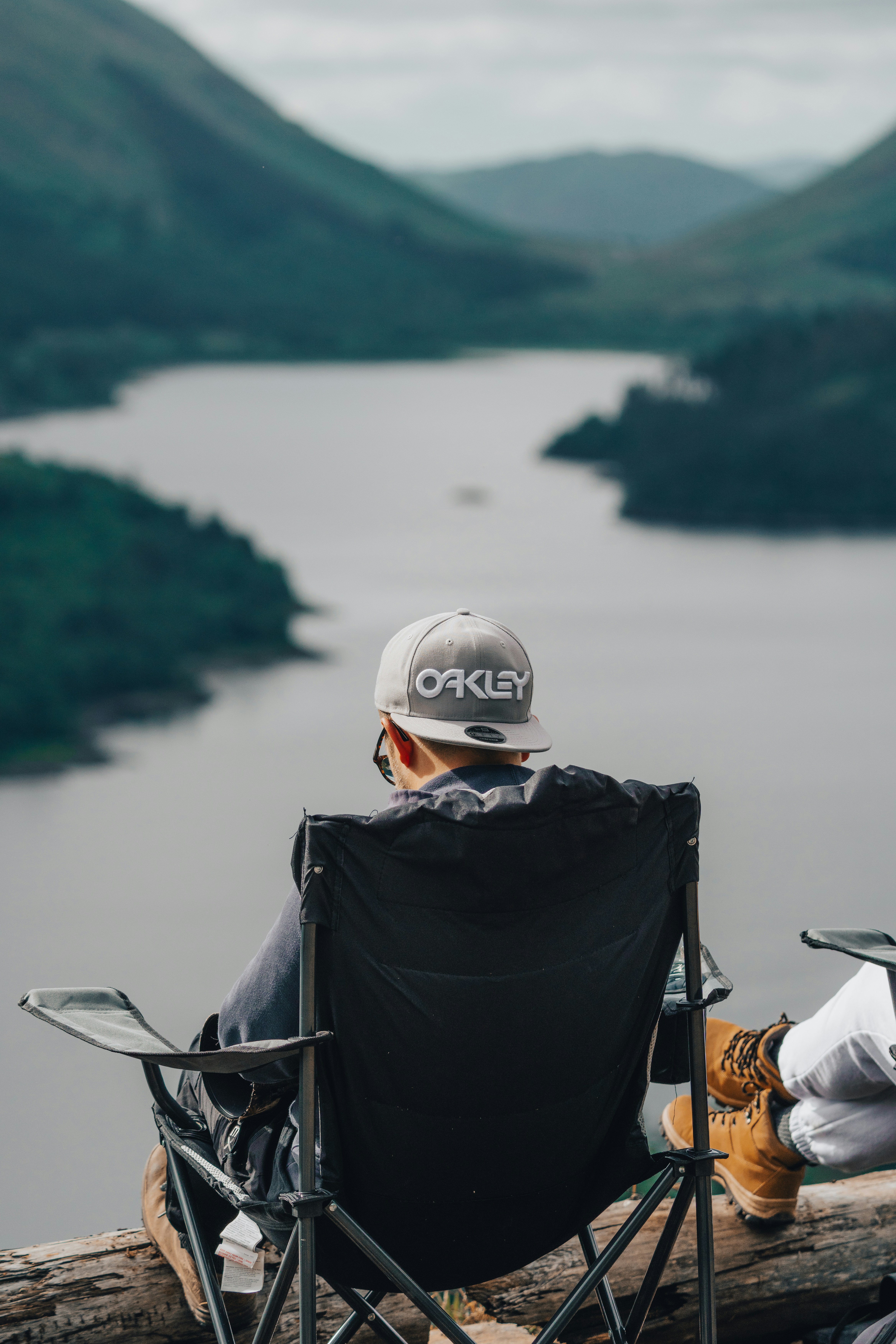 Edge of Solitude: A Lone Camper Seated on a Log, Gazing Over a Quiet Mountain Lake