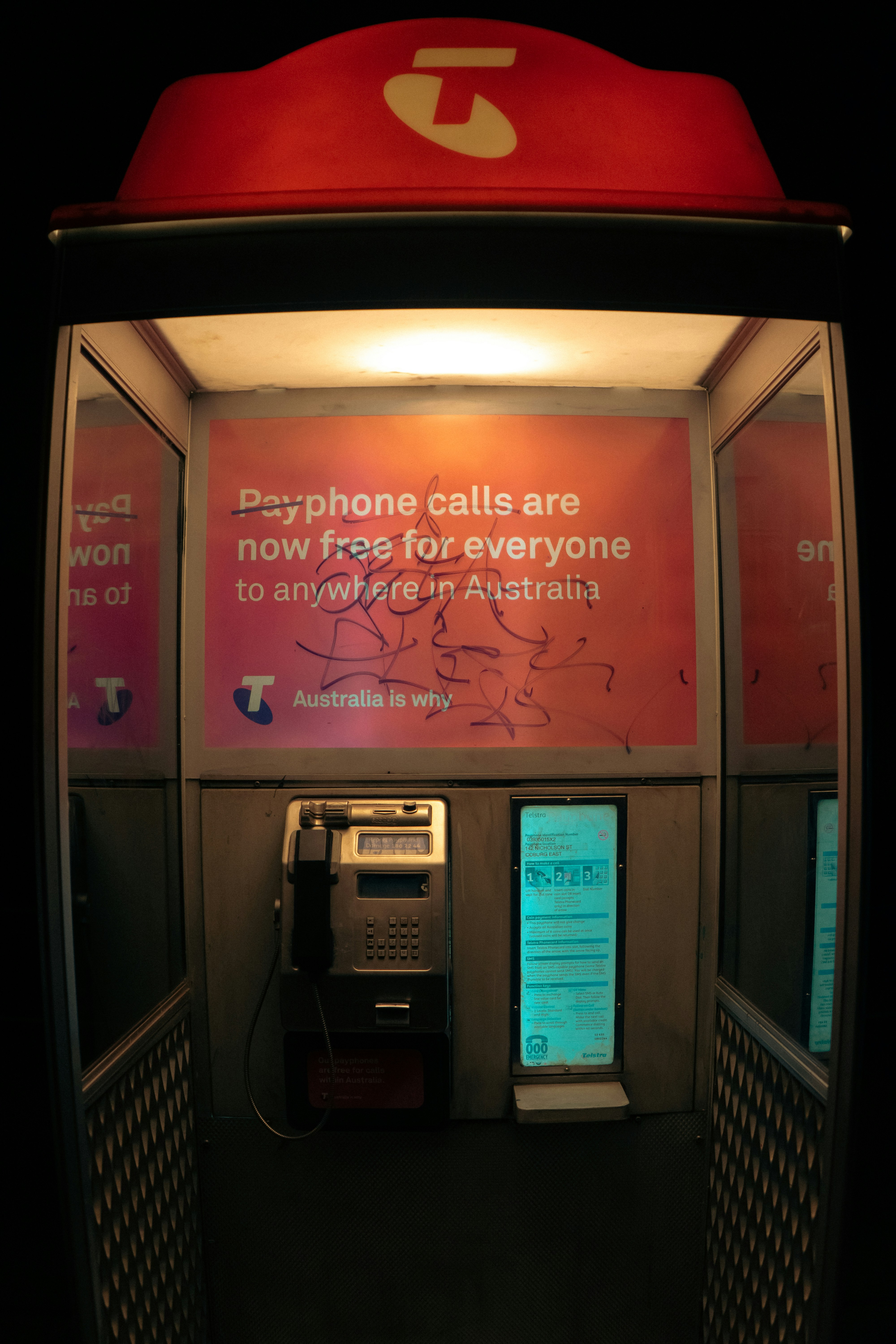 Red Public Phone Booth at Night with Graffiti and Poster
