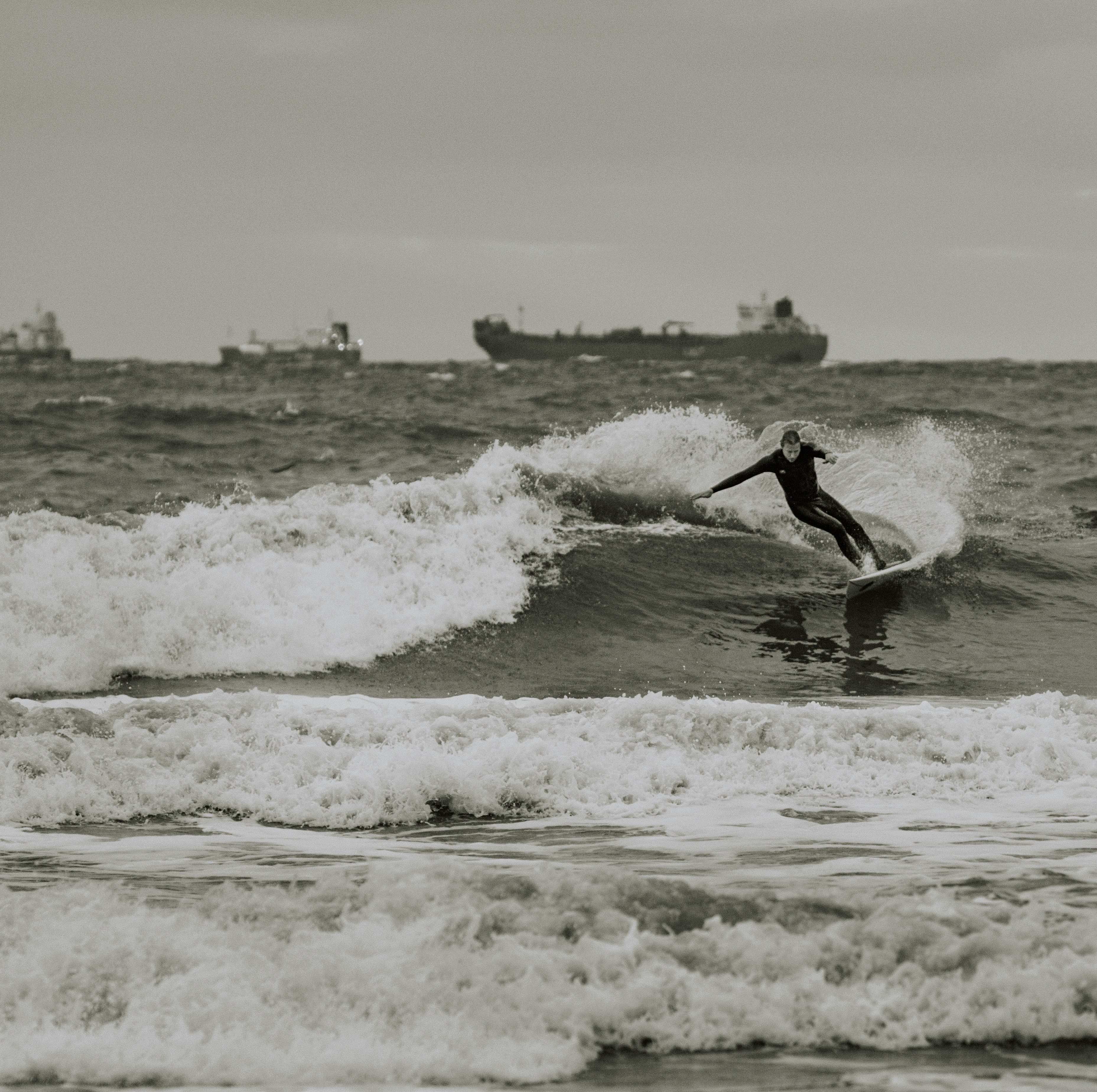 Monochrome Crest: Surfer Carves a Break as Freighters Watch from the Horizon