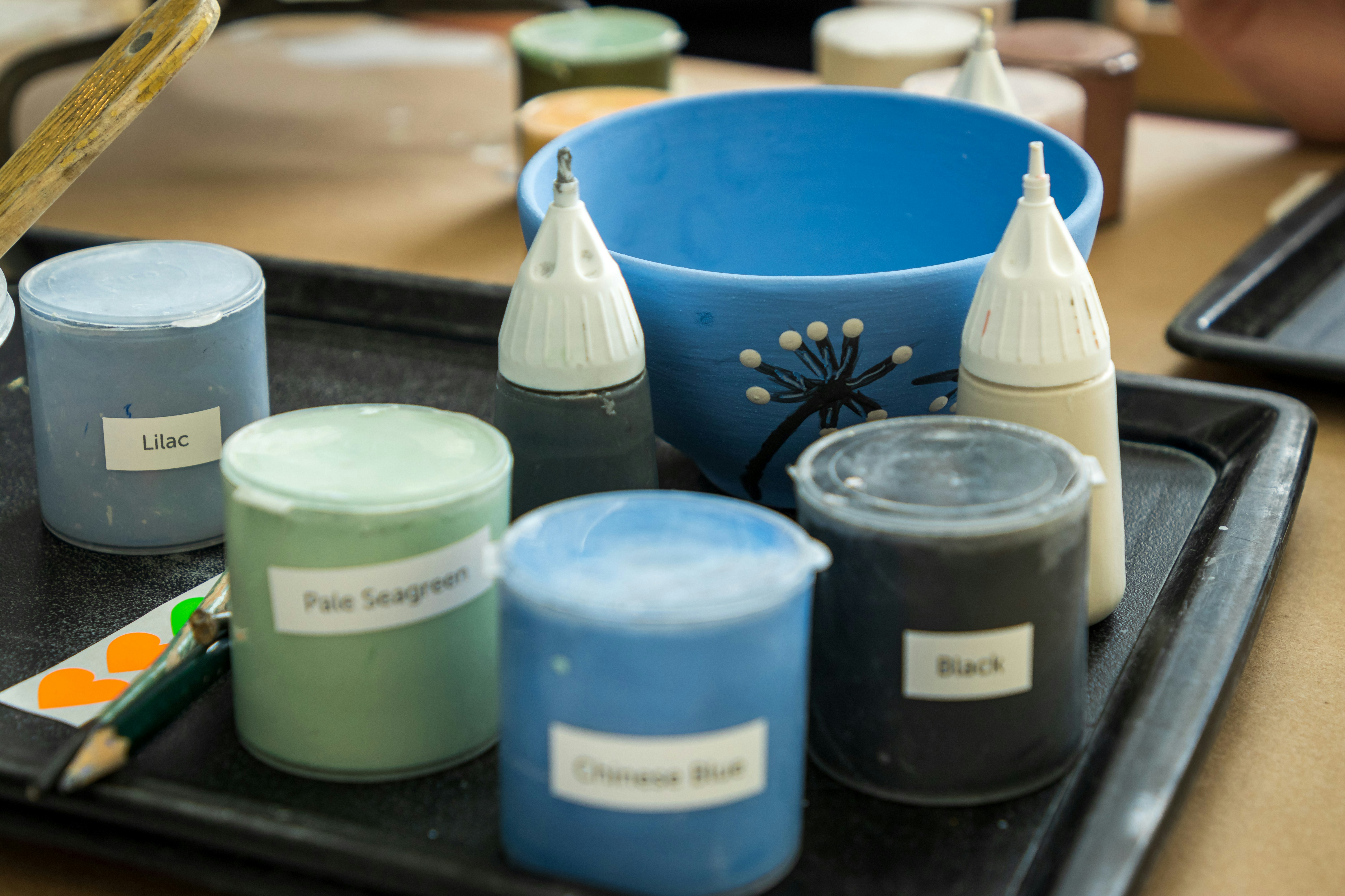 Assorted paint containers with labels, accompanied by a decorative blue bowl, arranged on a tray. A glimpse into an artist's workspace.