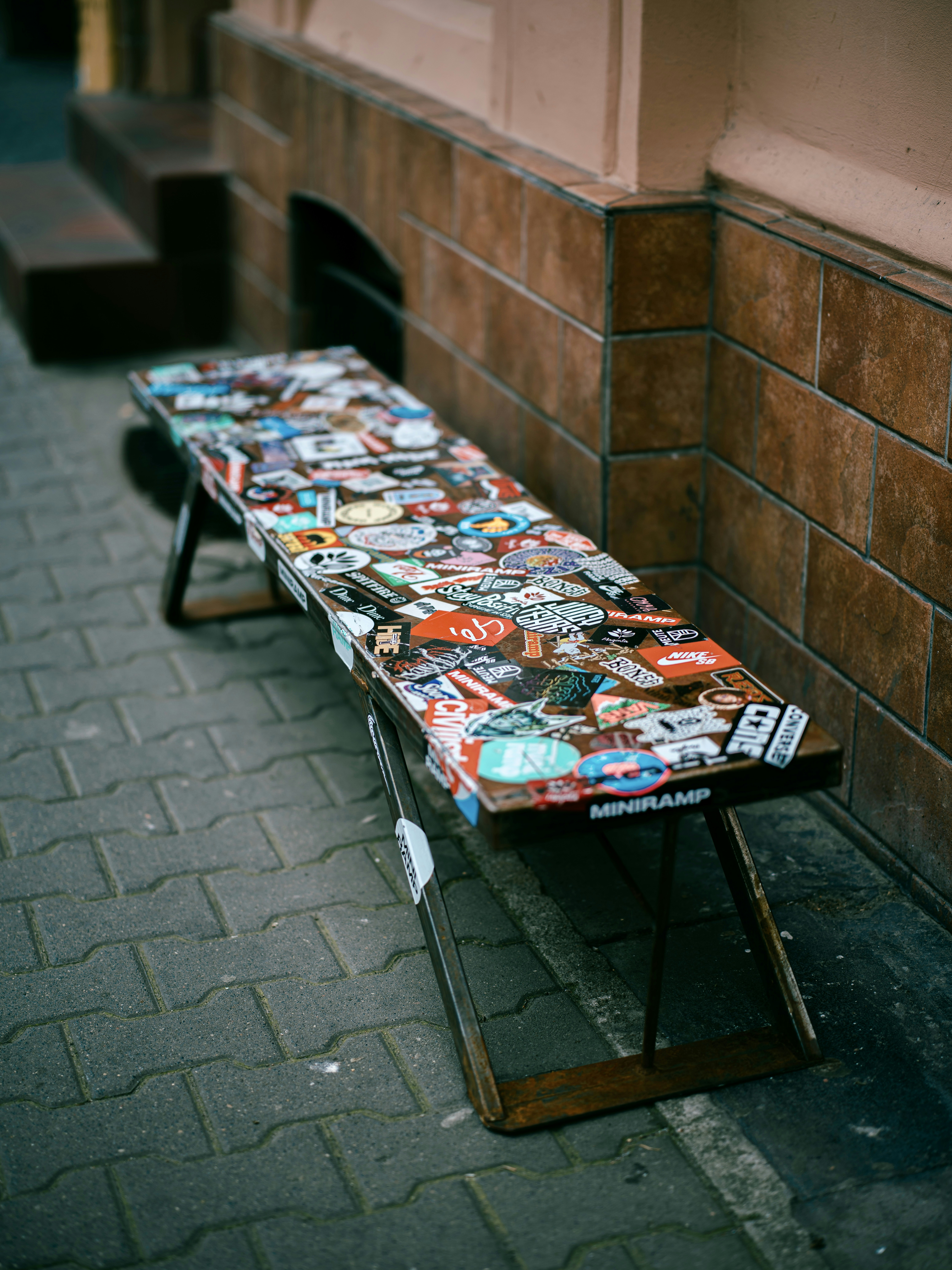 Colorful bench adorned with an eclectic mix of stickers, nestled against a textured wall in an urban setting.