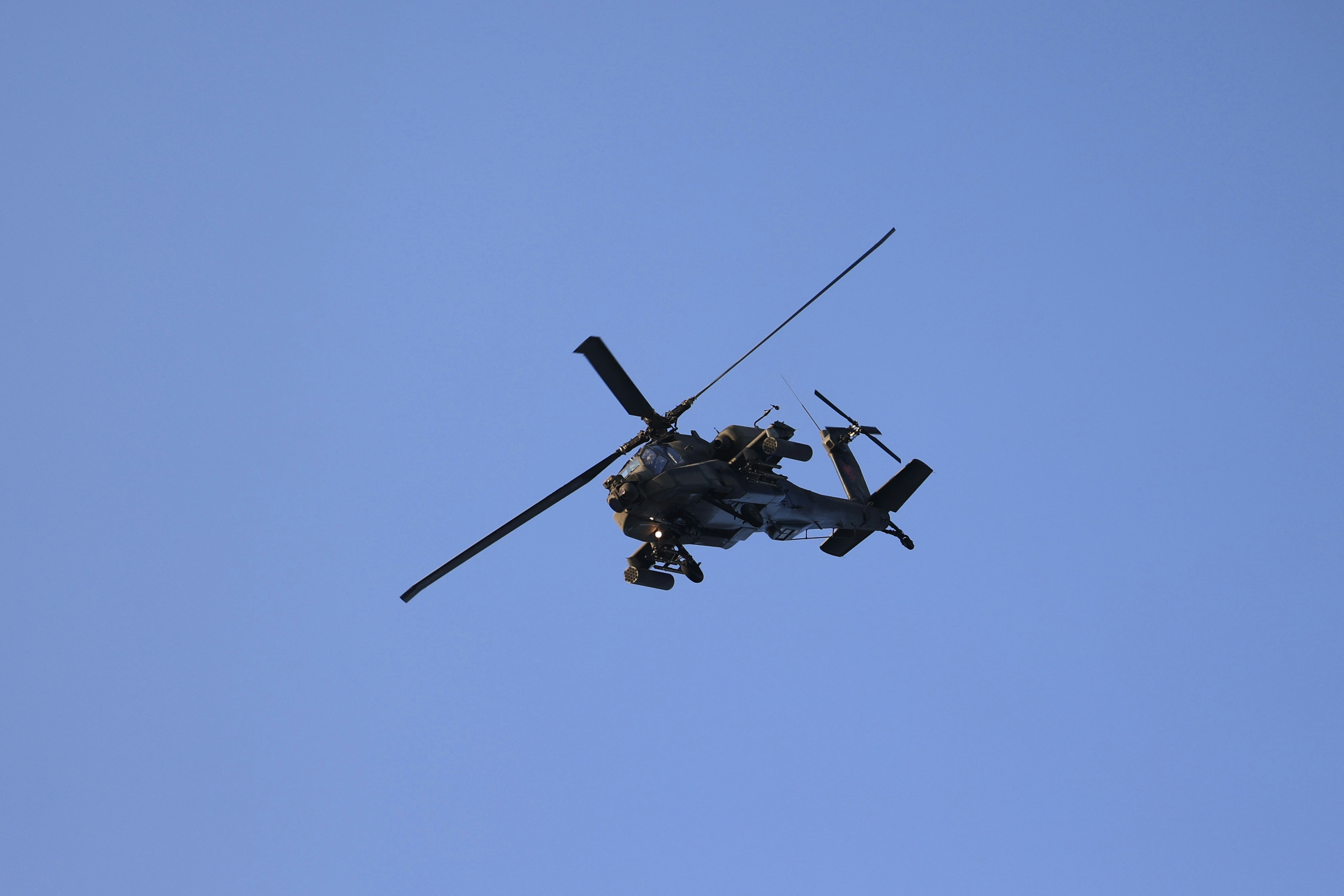 Military helicopter soaring through a clear blue sky.