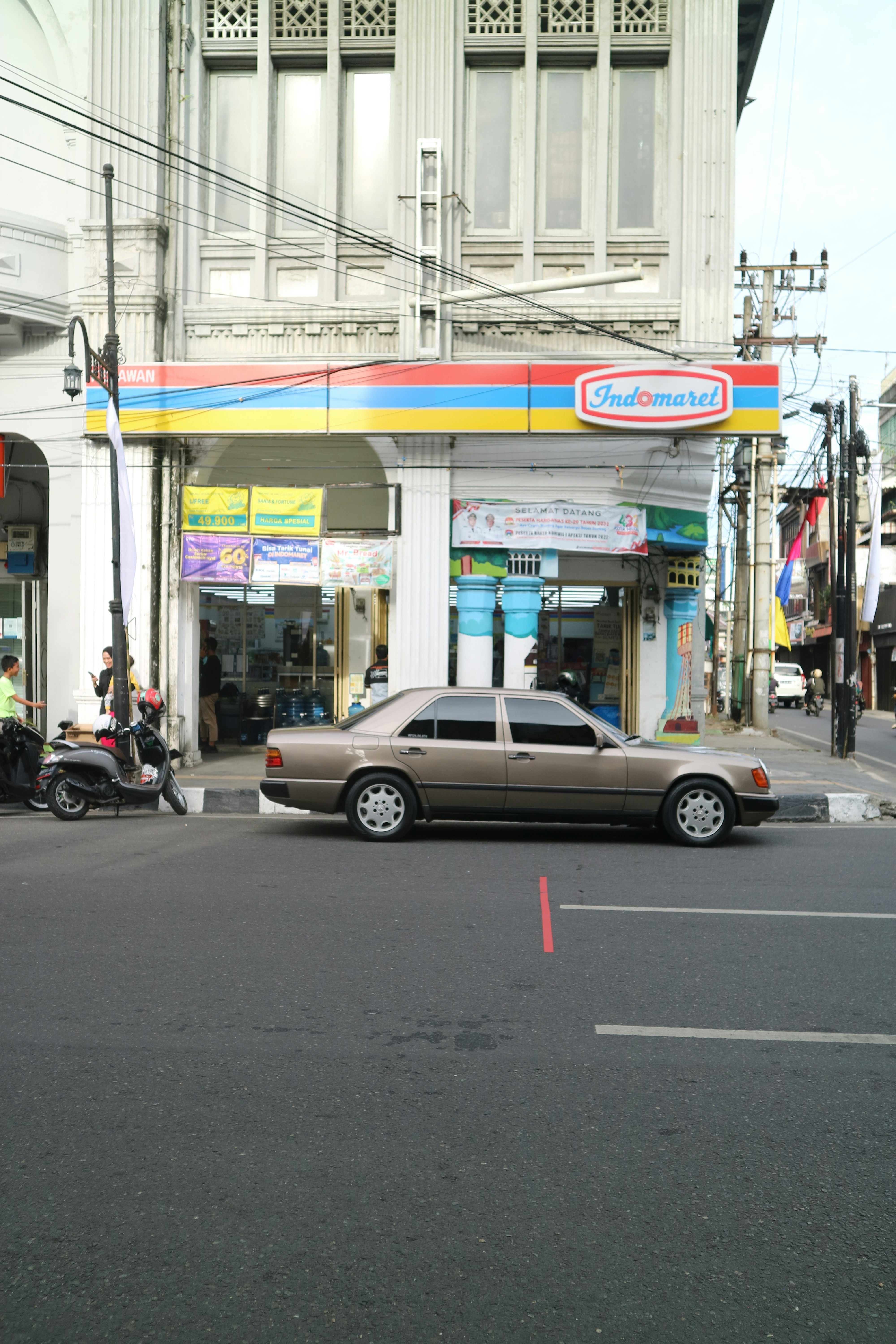 Curbside Pause: Beige Sedan in Front of Indomaret