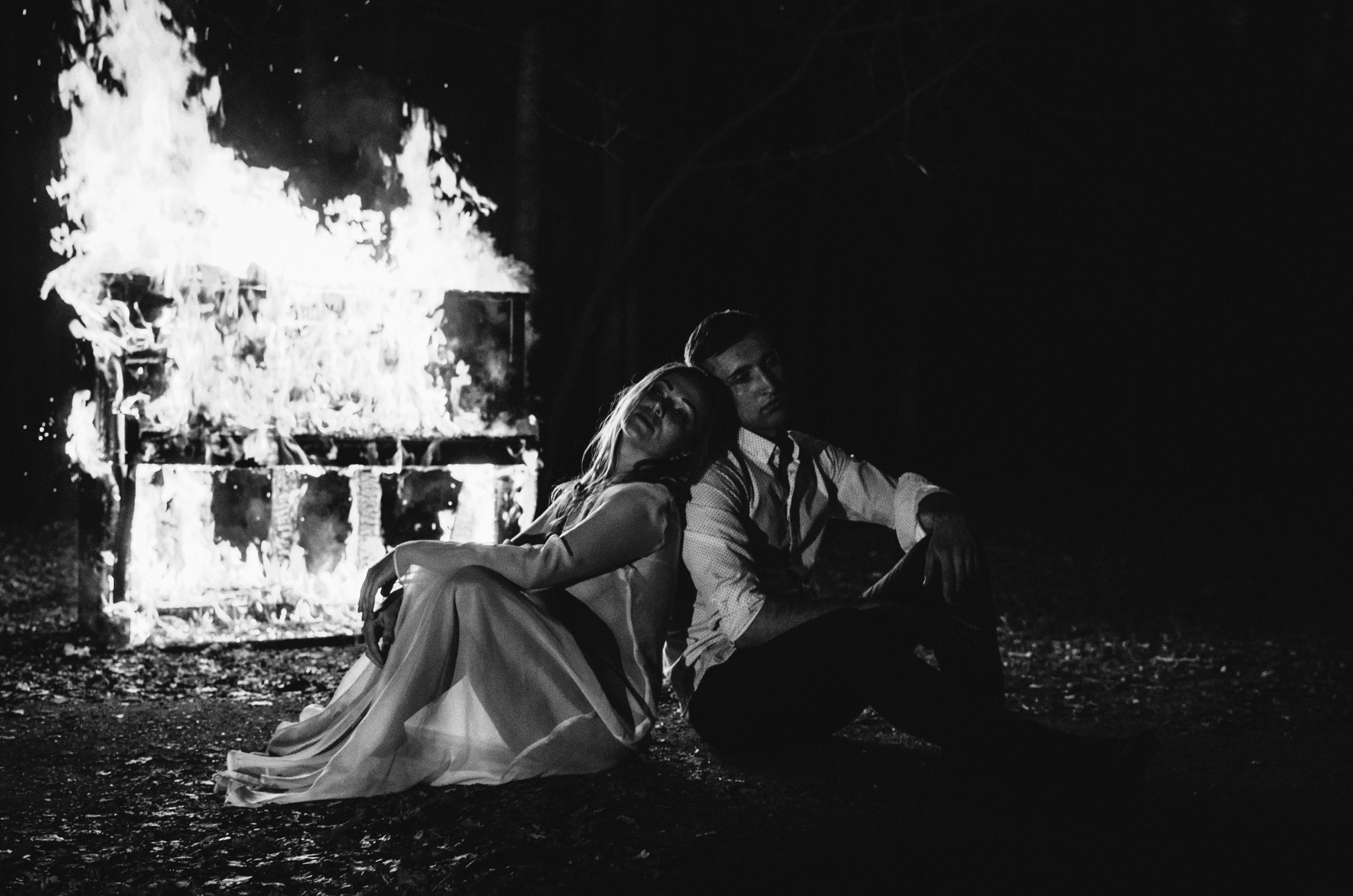 a man and woman sitting next to a large fire