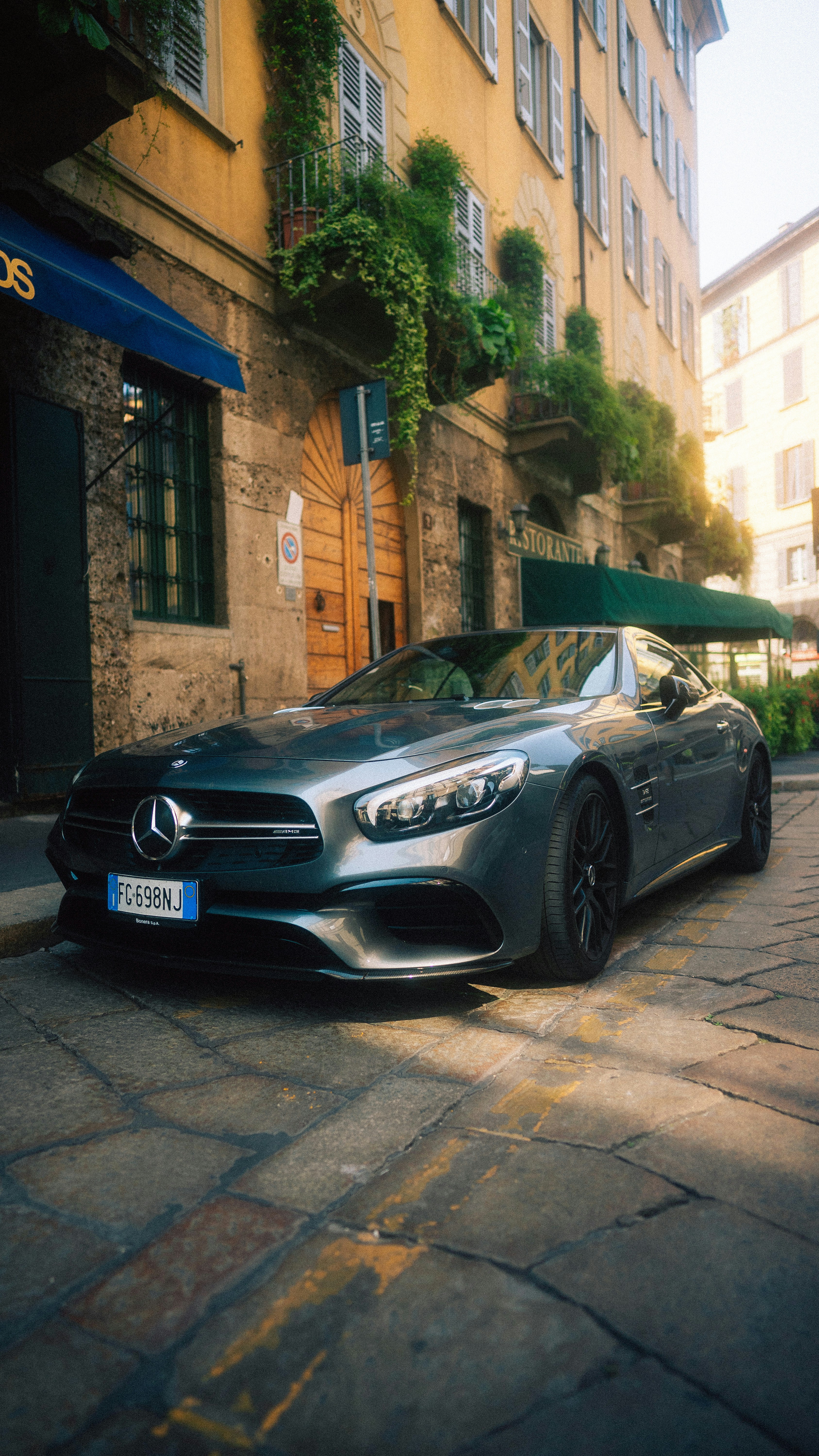 Sleek Mercedes SL parked on a cobblestone street, framed by historic buildings adorned with greenery. The scene captures a blend of luxury and classic architecture.