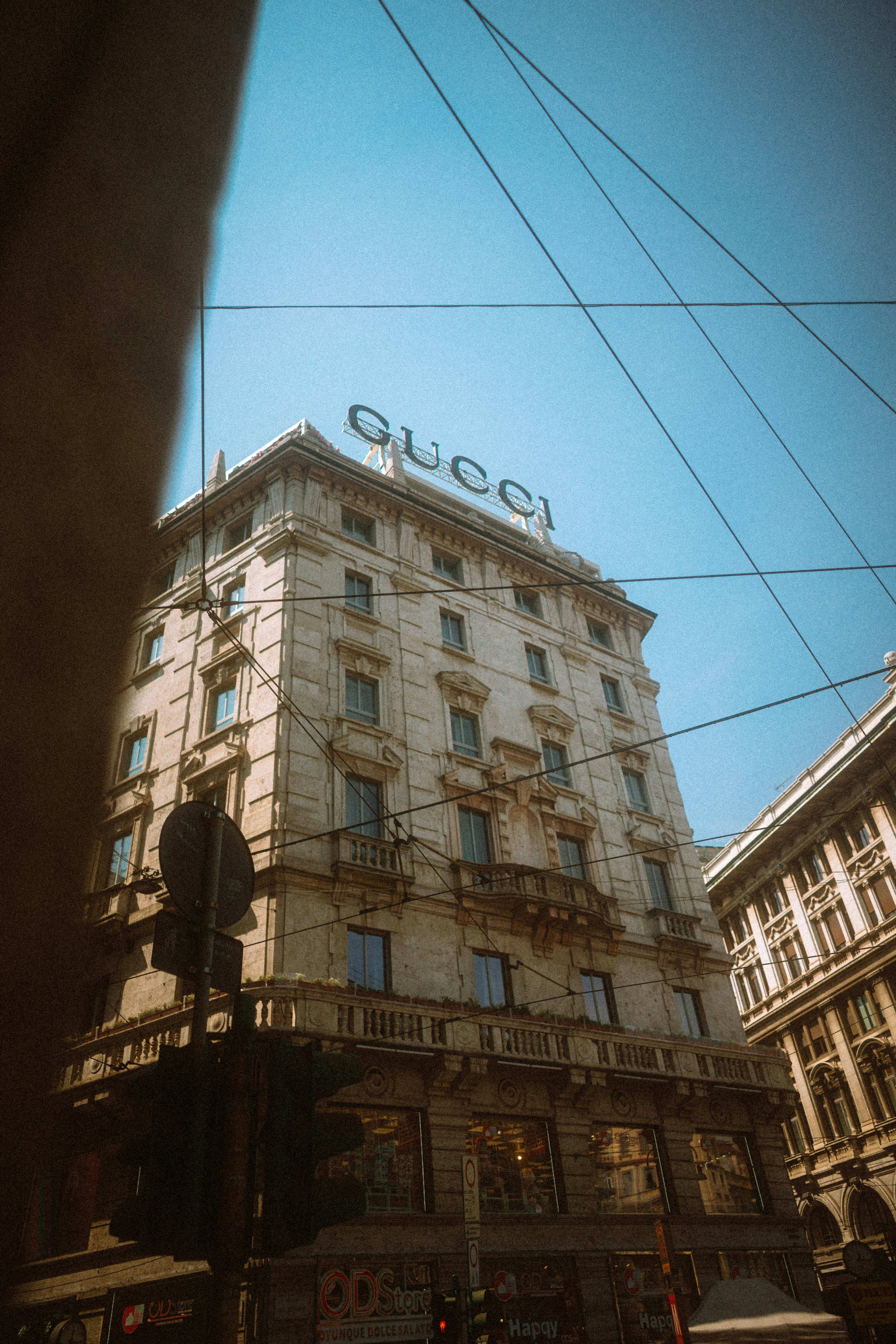 Gucci Sign Crowned Over a Sunlit Historic Facade in a Busy City Block
