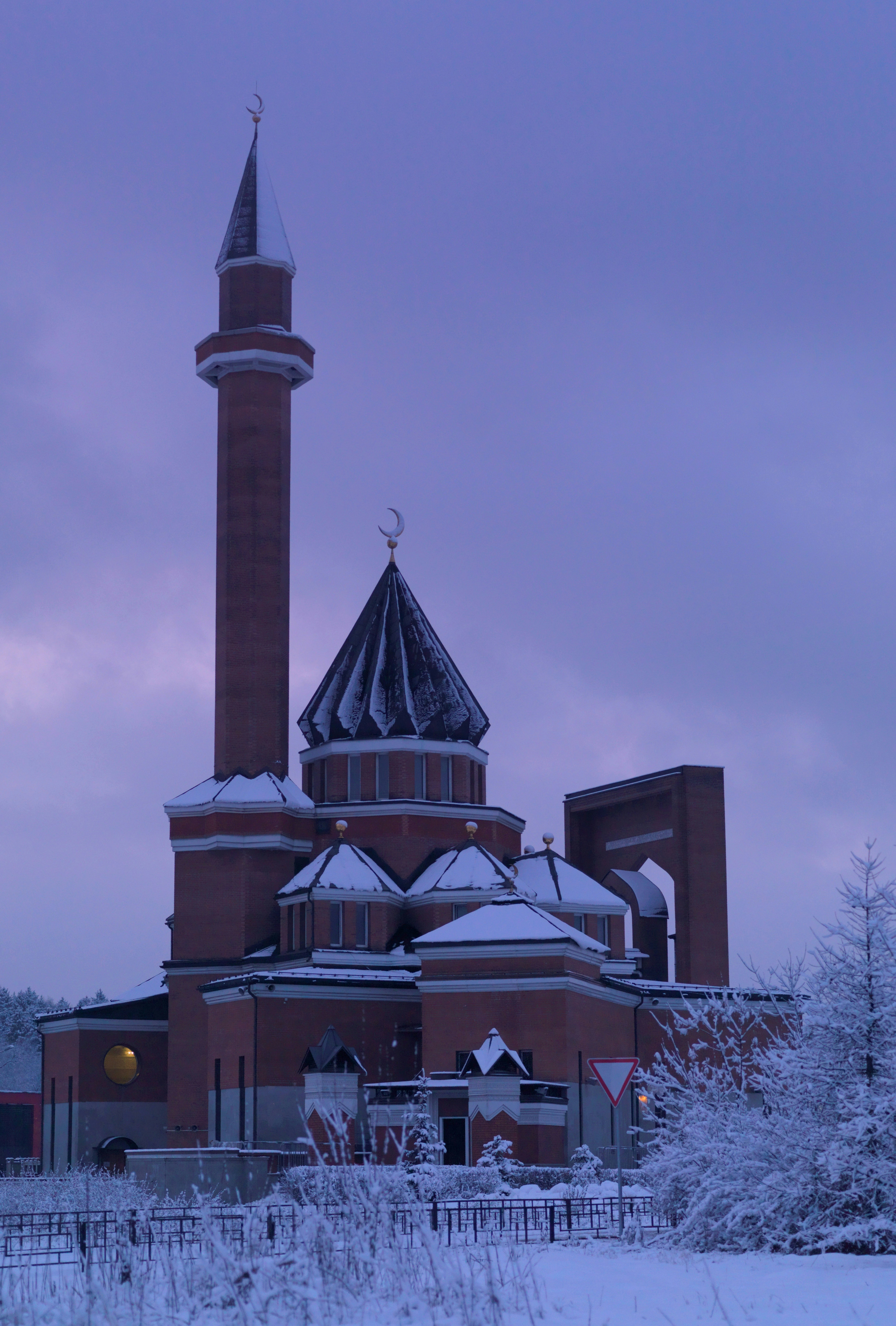 A mosque adorned with snow, showcasing its intricate architecture against a twilight sky. The scene captures a tranquil winter atmosphere.