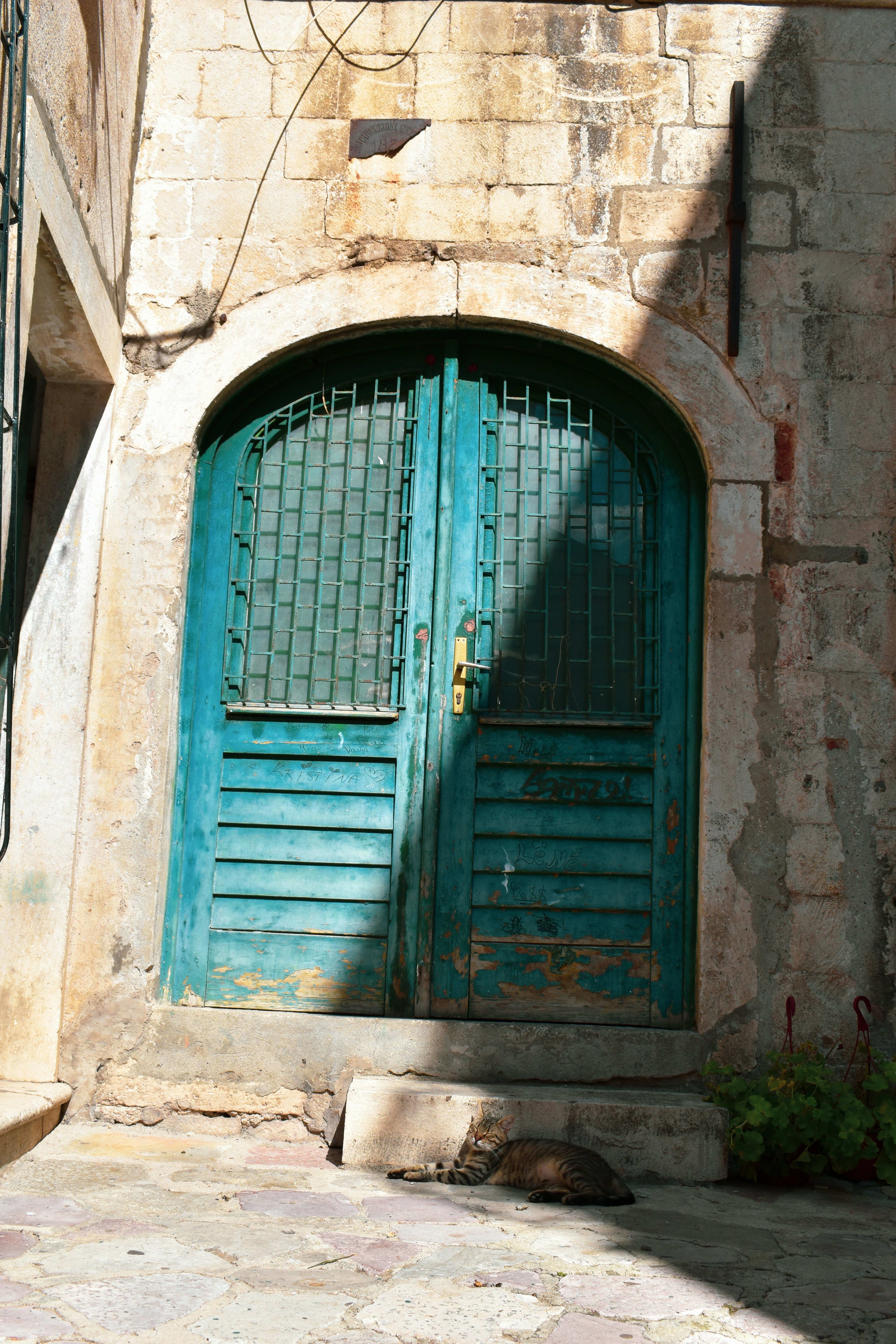Teal Gate in Stone Archway: Sunlit Silence with a Dozing Cat