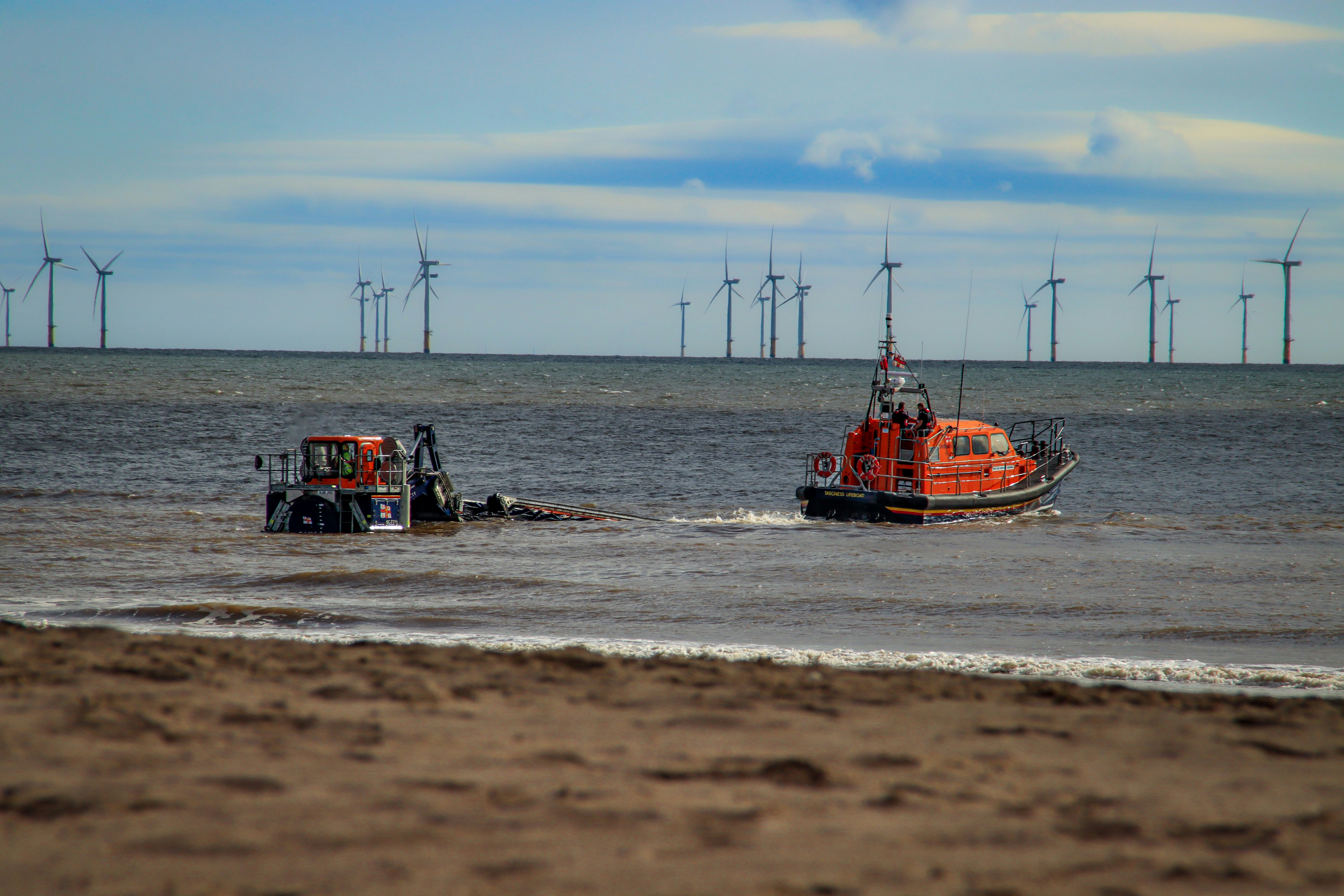 Red Rescue Boat Leads the Seascape Under a Line of Offshore Wind Turbines