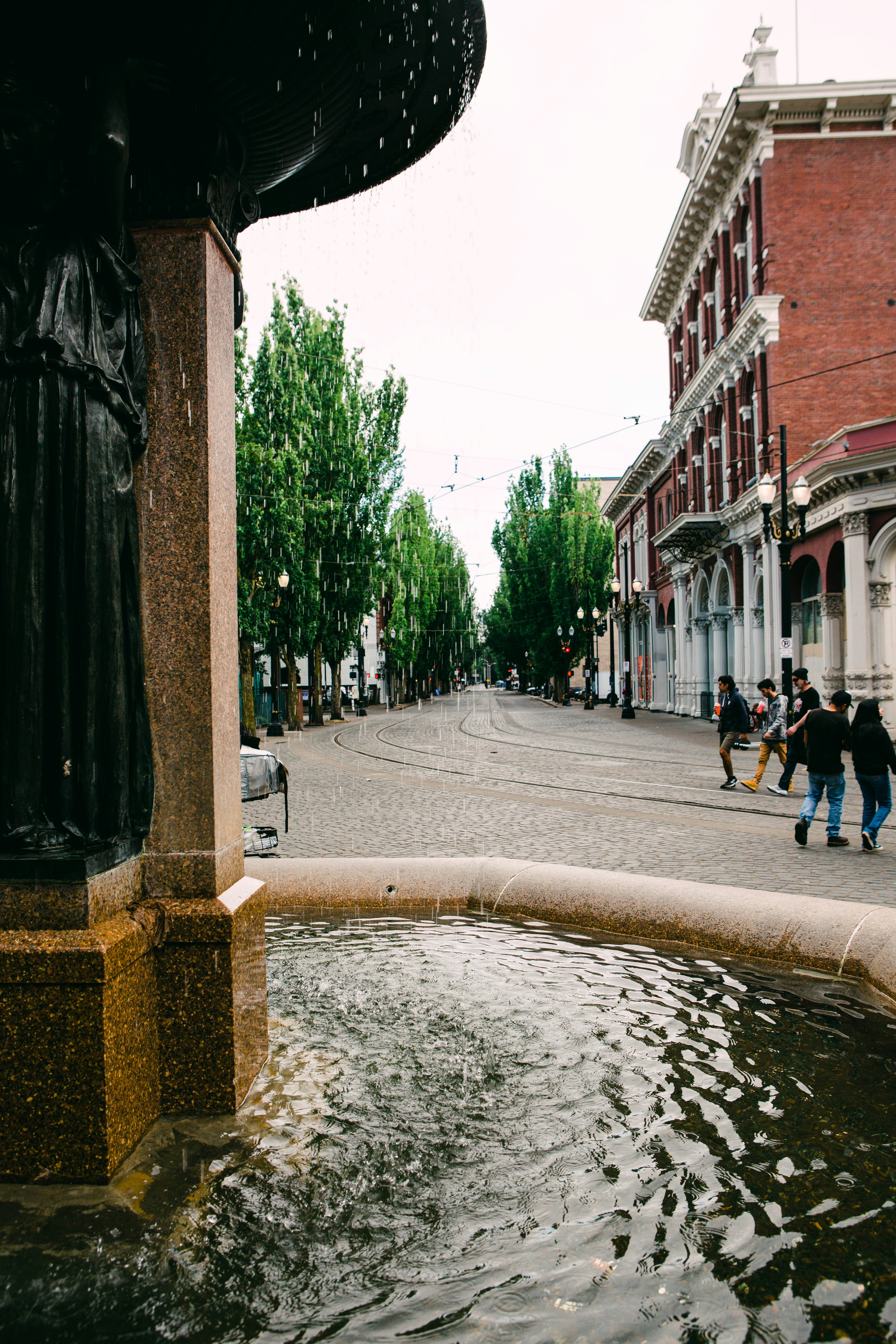 a group of people walking on a sidewalk next to a fountain