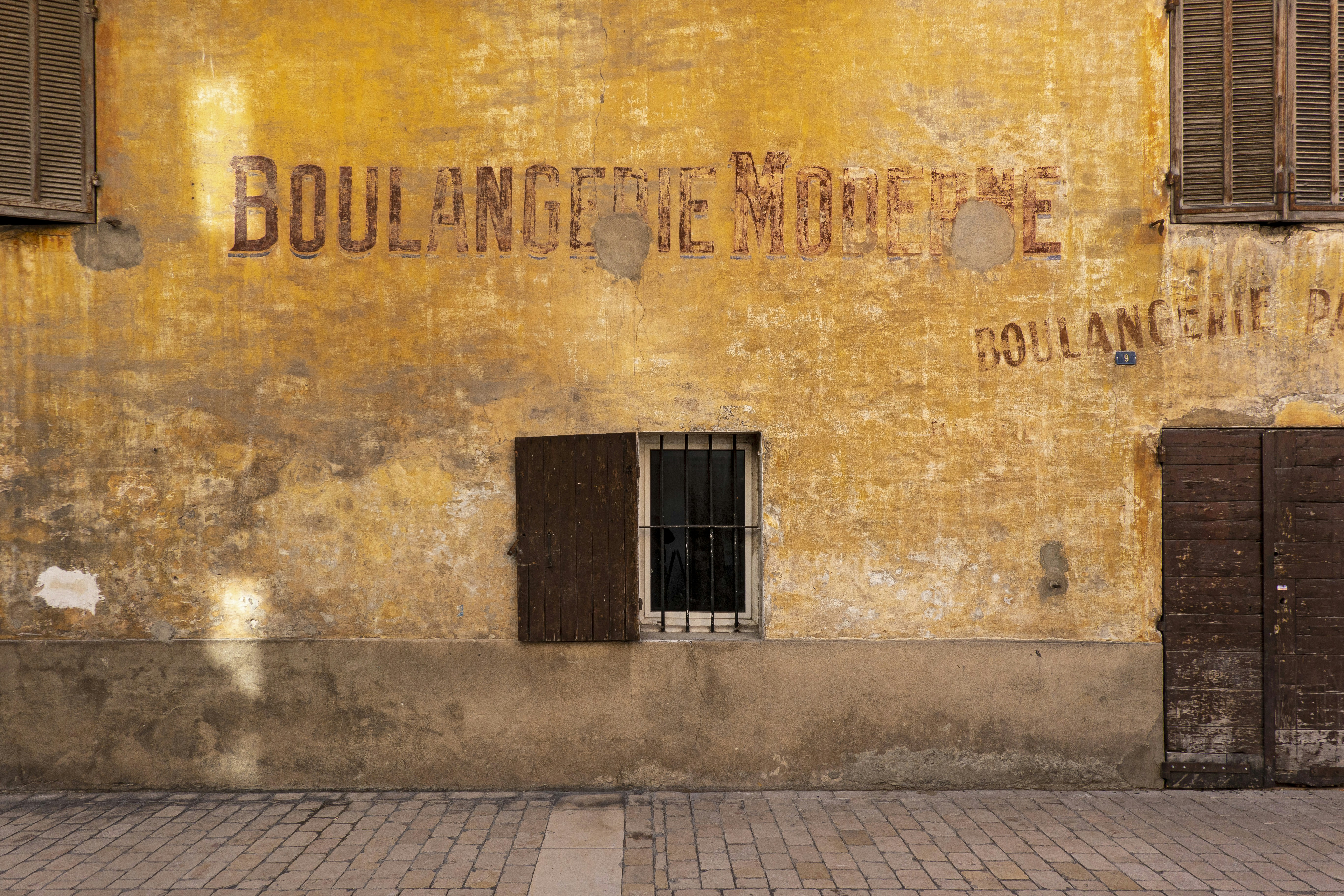 Aged Boulangerie Facade: Sunlit Yellow Wall with a Faded Sign