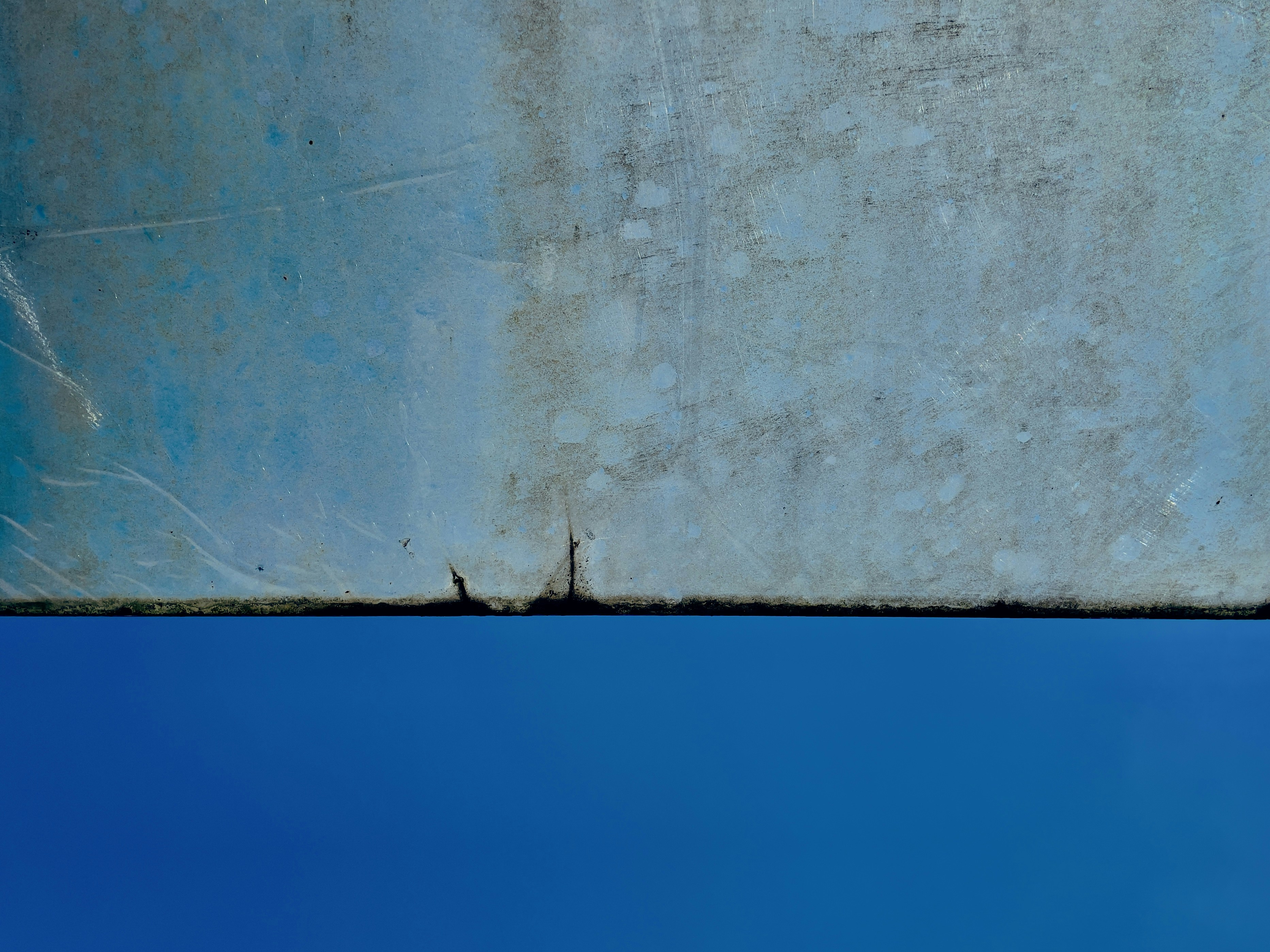 A textured blue surface meets a deep azure sky, creating a striking contrast between the two elements. The subtle imperfections add character to the scene.