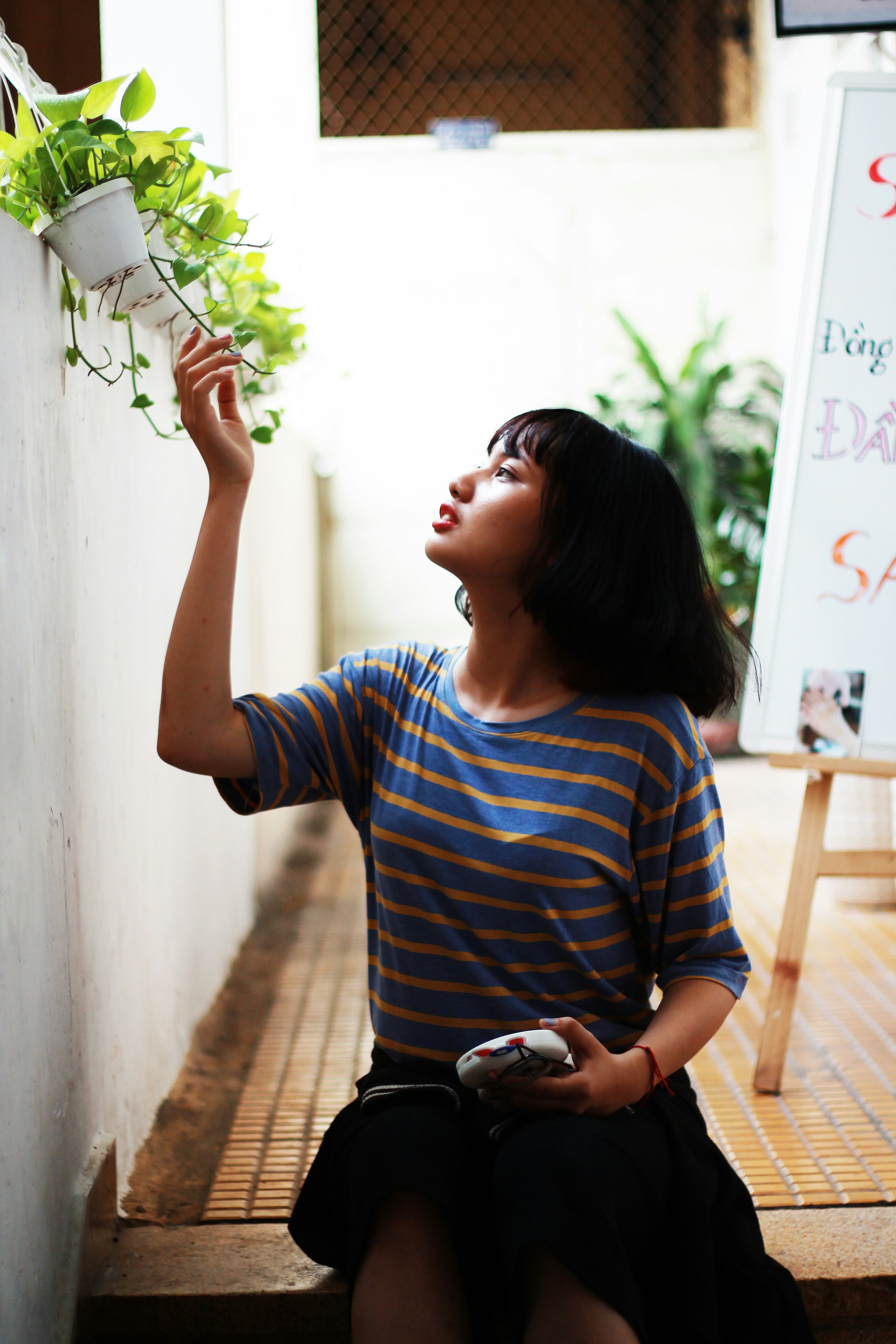 Green Touch: A Portrait Reaching Toward a Hanging Plant in a Sunlit Corridor