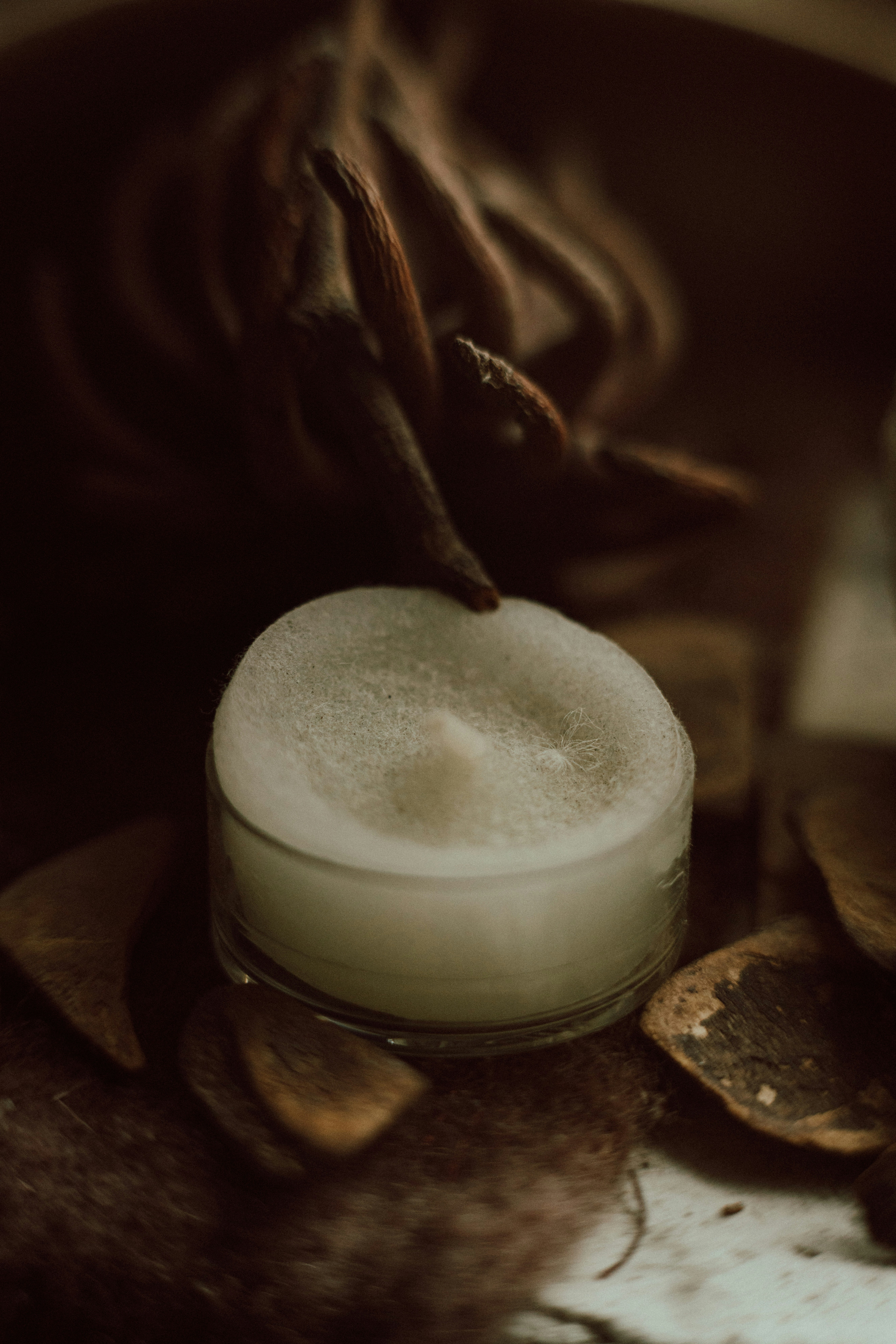 A softly glowing candle rests among natural elements, creating a tranquil atmosphere. The warm tones and textures invite a sense of calm.