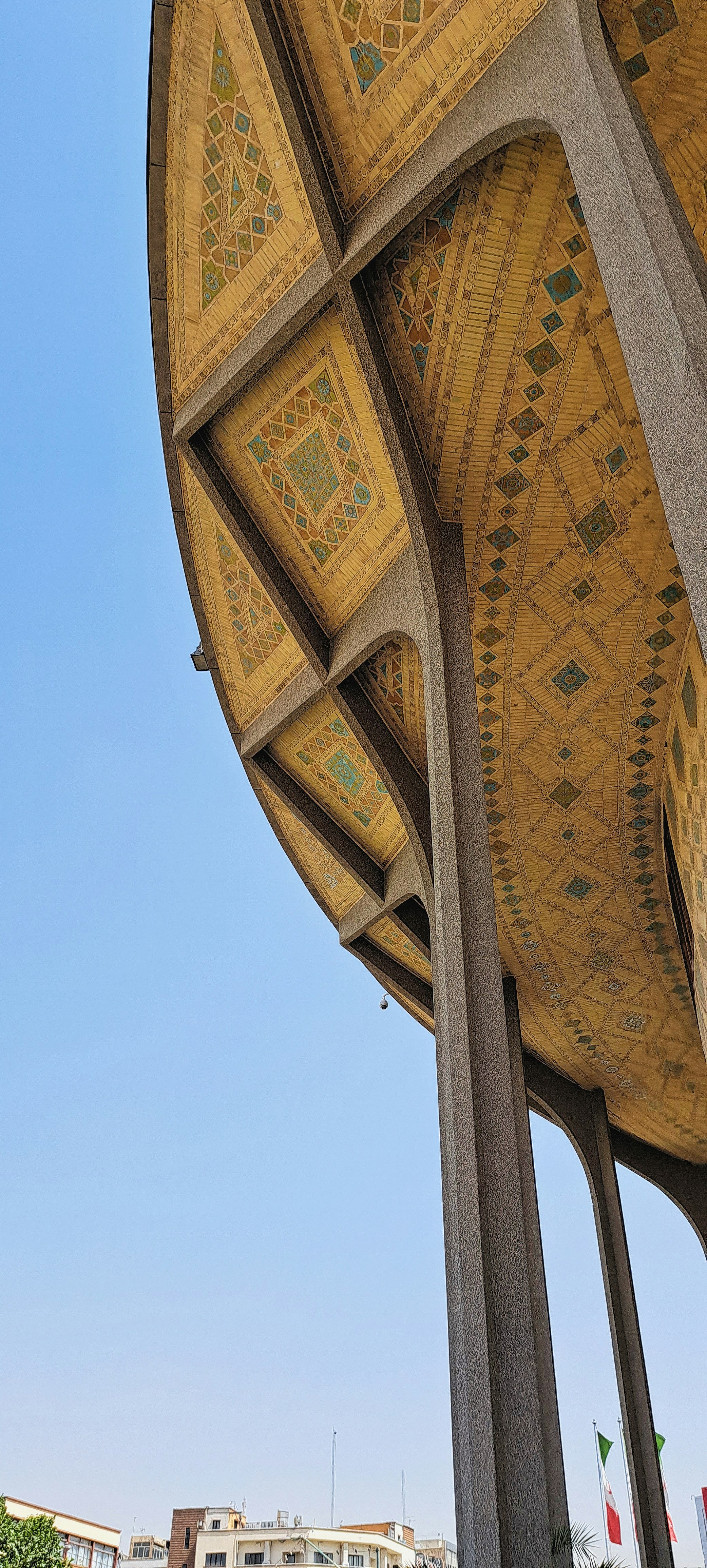 Intricate ceiling details of a modern architectural structure under a clear blue sky. The design showcases geometric patterns and vibrant colors.