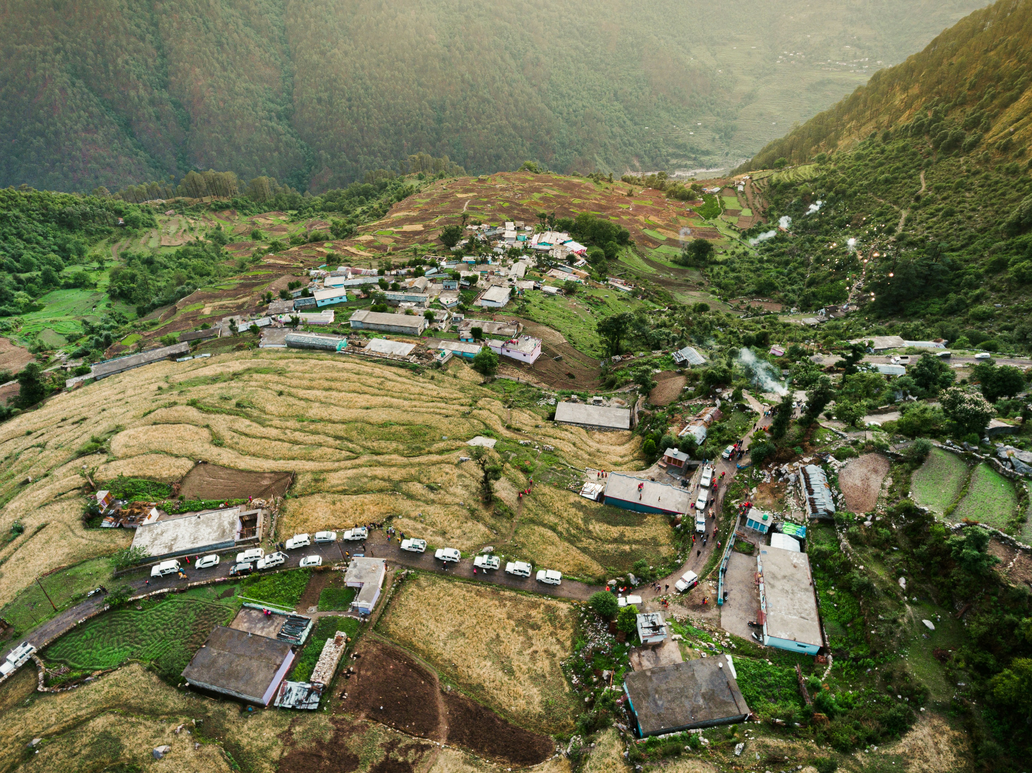 Aerial view of a rural village nestled in lush hills, showcasing agricultural fields and homes. The scene captures the essence of community living in harmony with nature.