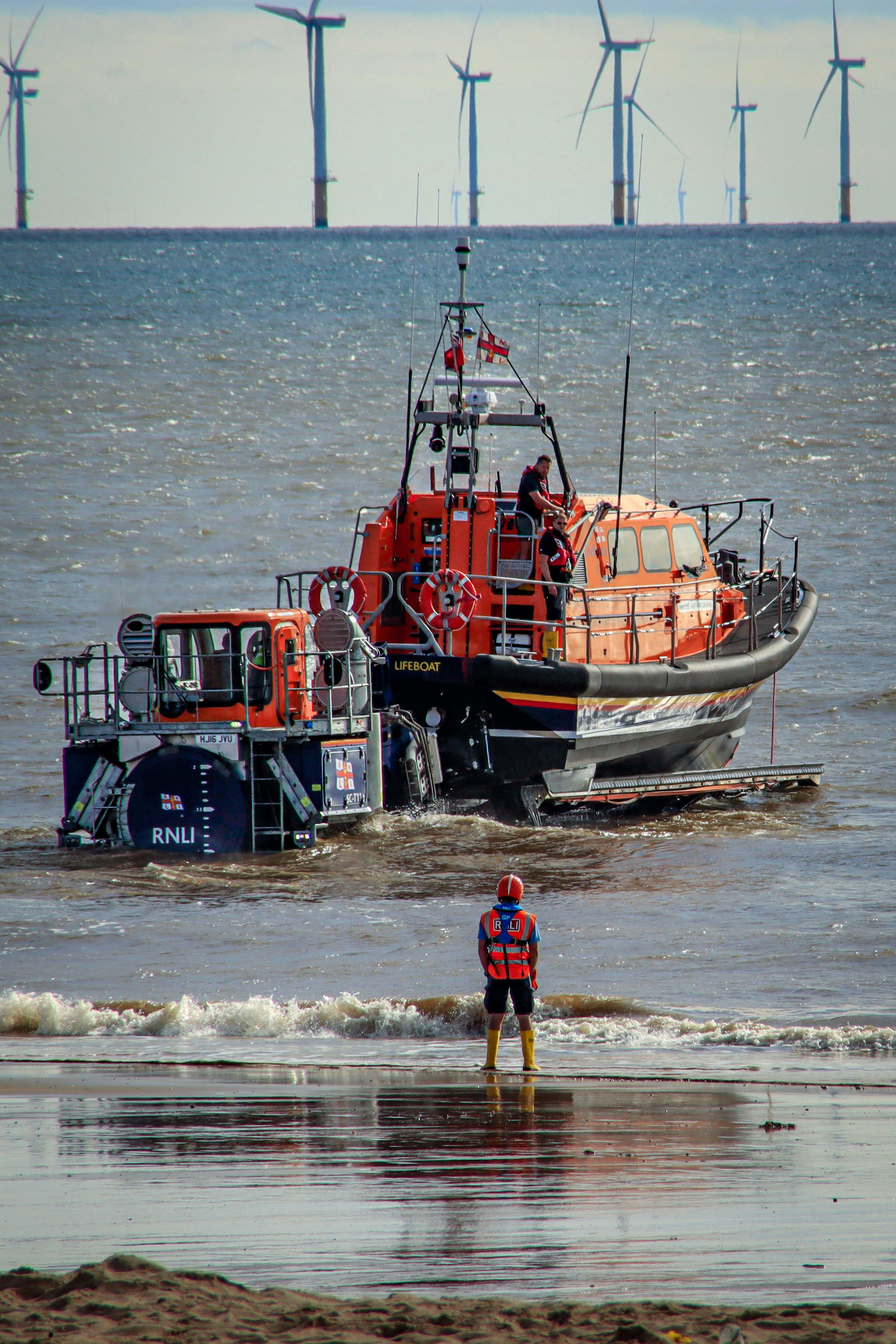 Red Lifeboat at Low Tide: Duty, Dawn, and a Distant Wind-Farm Horizon