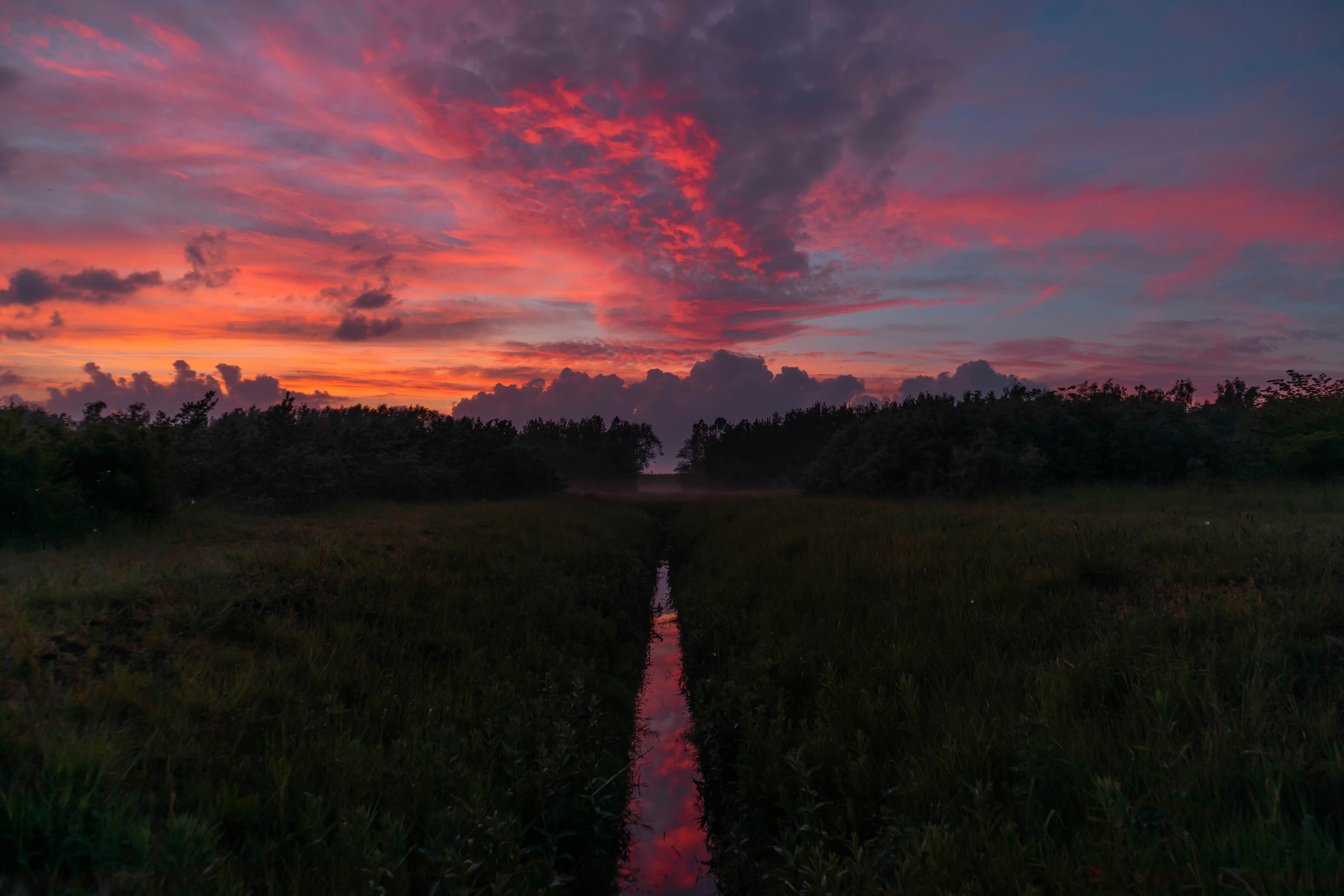 Sunset's Red Thread: A Narrow Ditch Winding Through Dusk-lit Grass