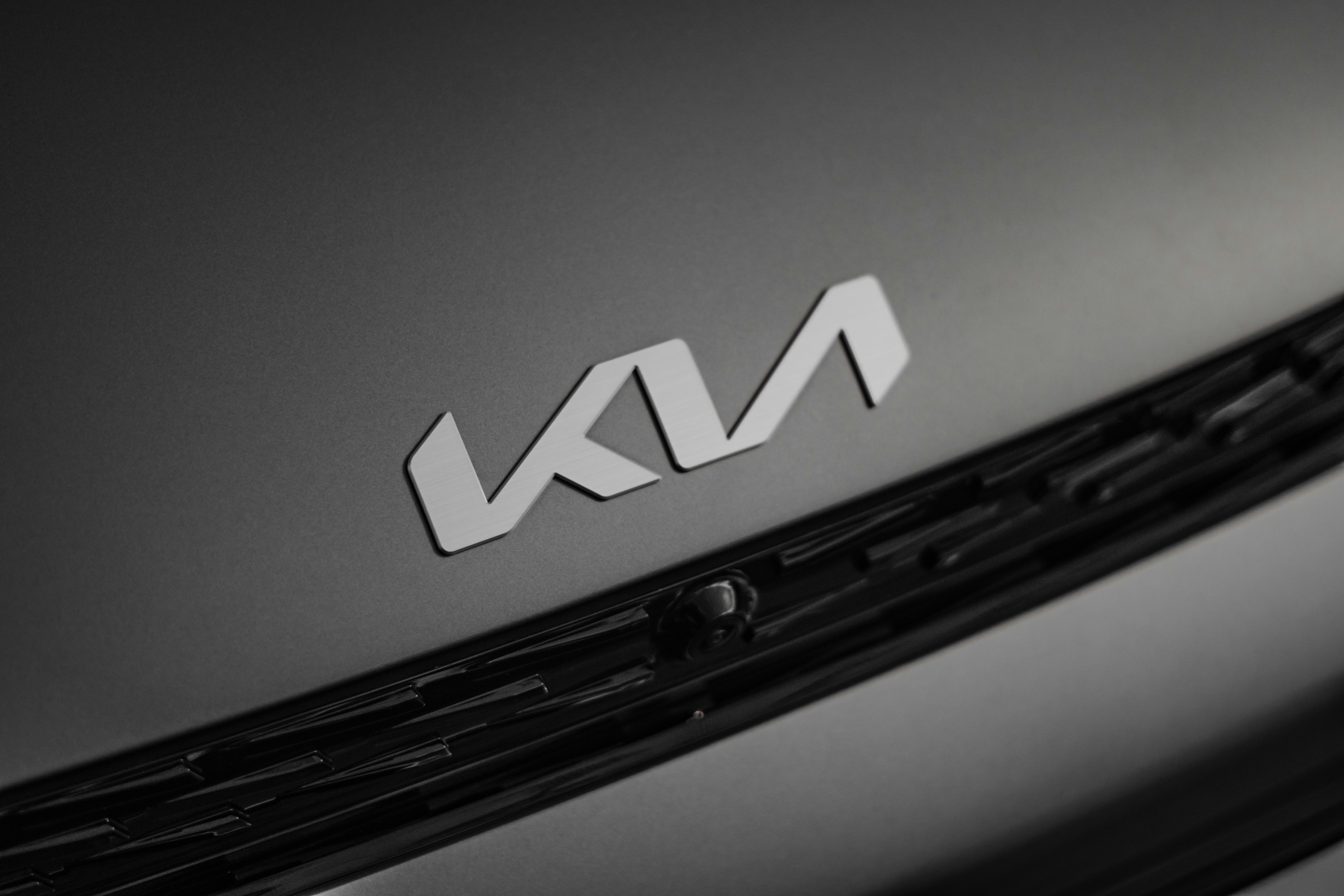 Close-up of the Kia logo on a sleek vehicle surface, showcasing modern design elements and branding.