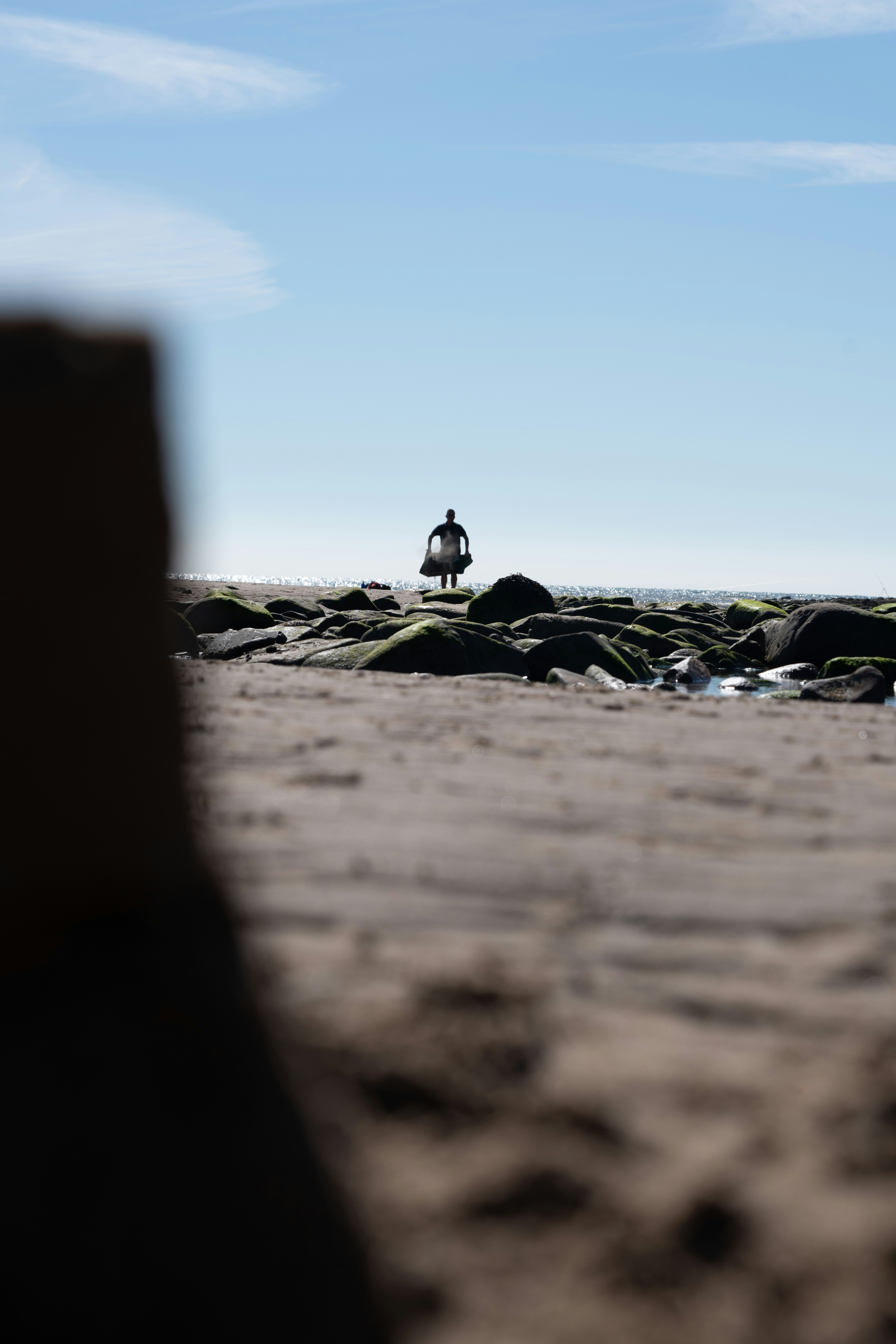 Edge of Calm: A Lone Figure with a Surfboard Crossing Mossy Rocks Toward the Sea