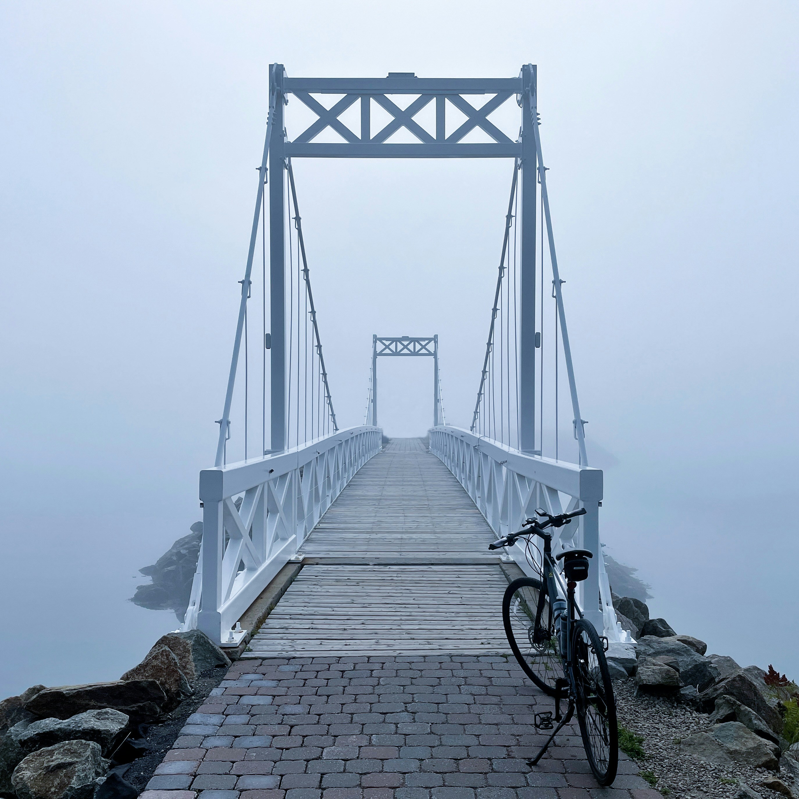 Mistbound Suspension: A lone cyclist guards the fog-locked bridge