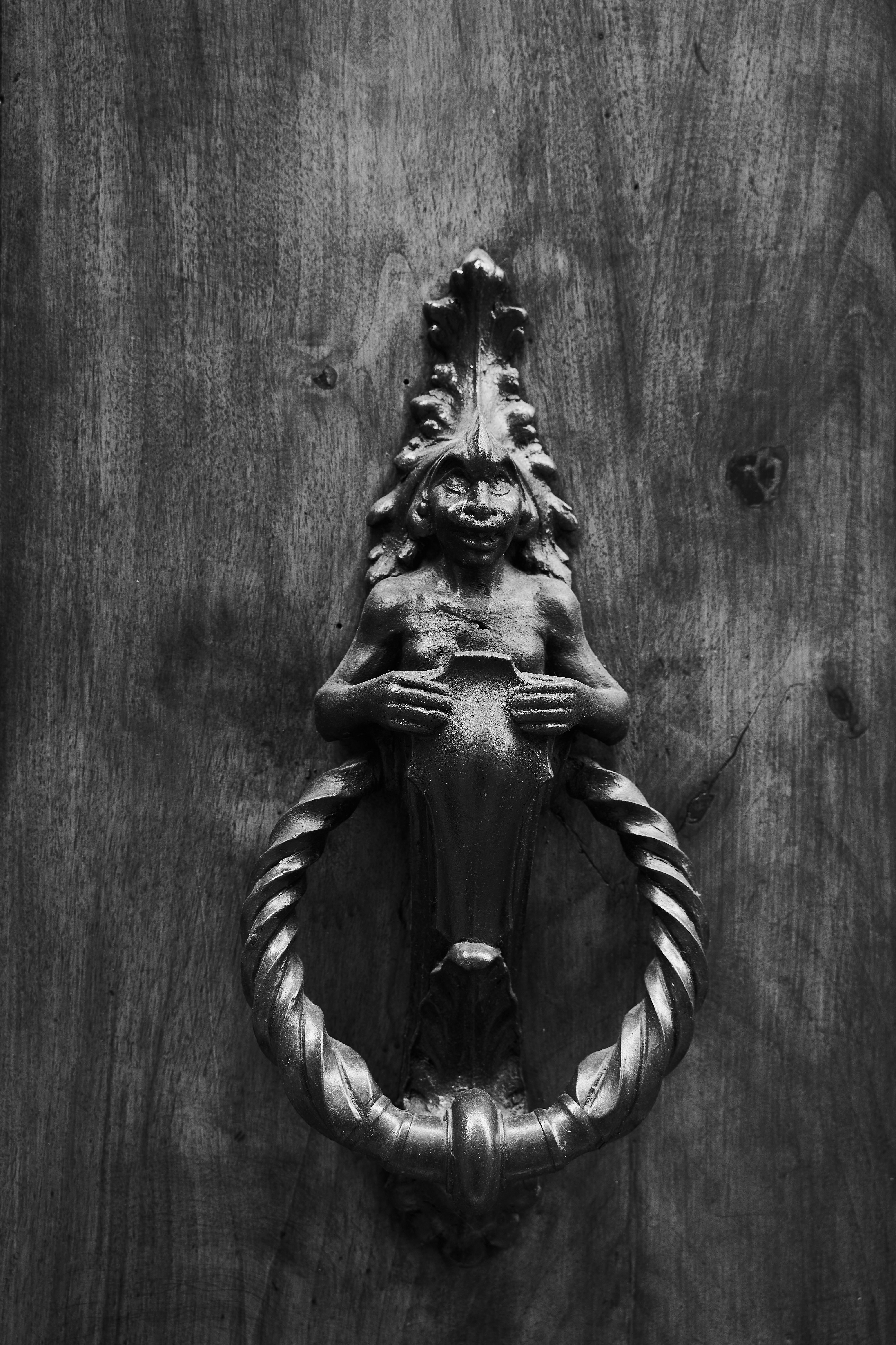 The Ring-Bearing Sentinel: Carved Figure Gripping a Ring on Weathered Wood