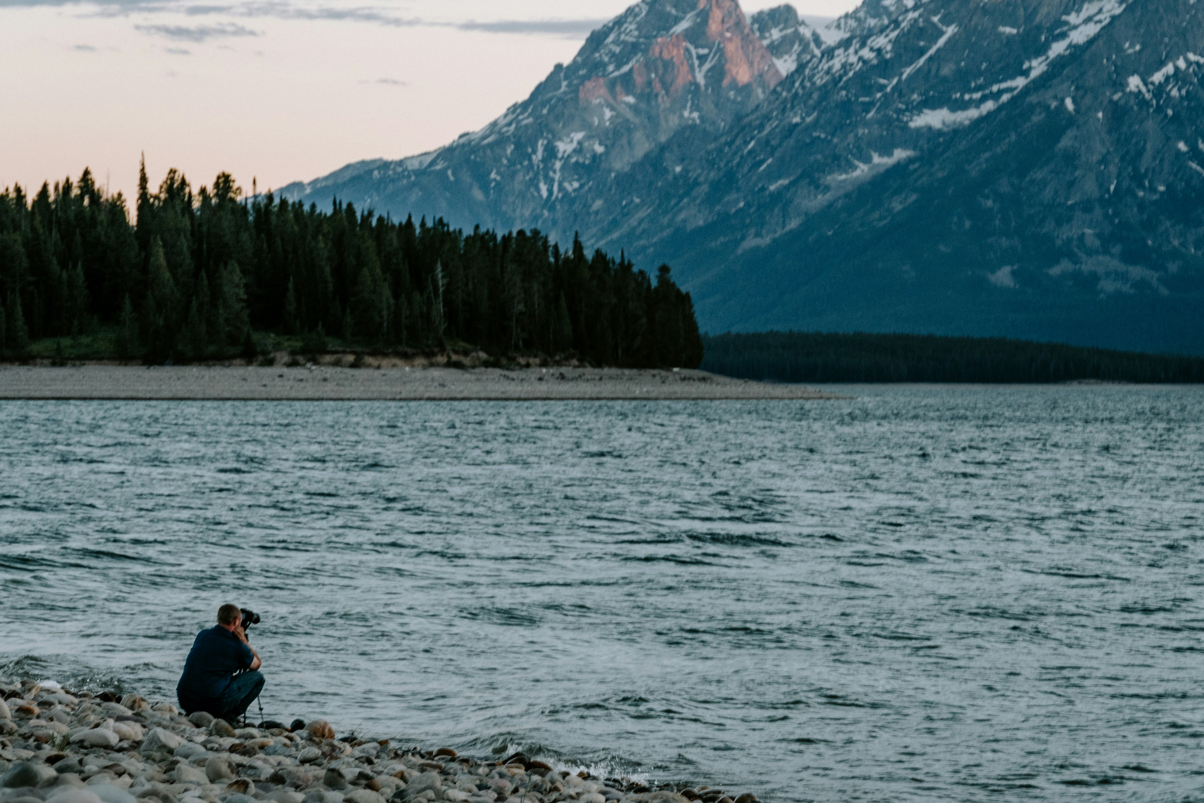 Solitude by the Shoreline: A lone figure on rocky banks with distant mountains