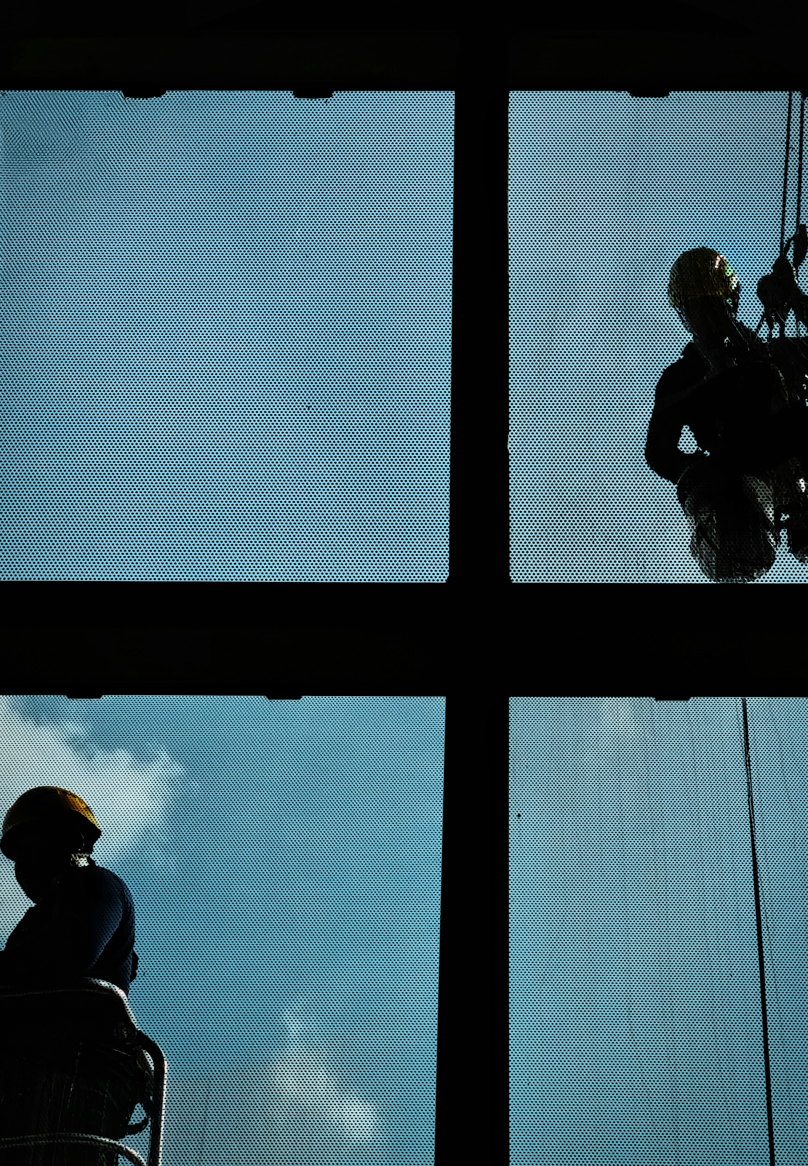 Silhouetted window cleaners working against a bright blue sky, framed by large glass panes.