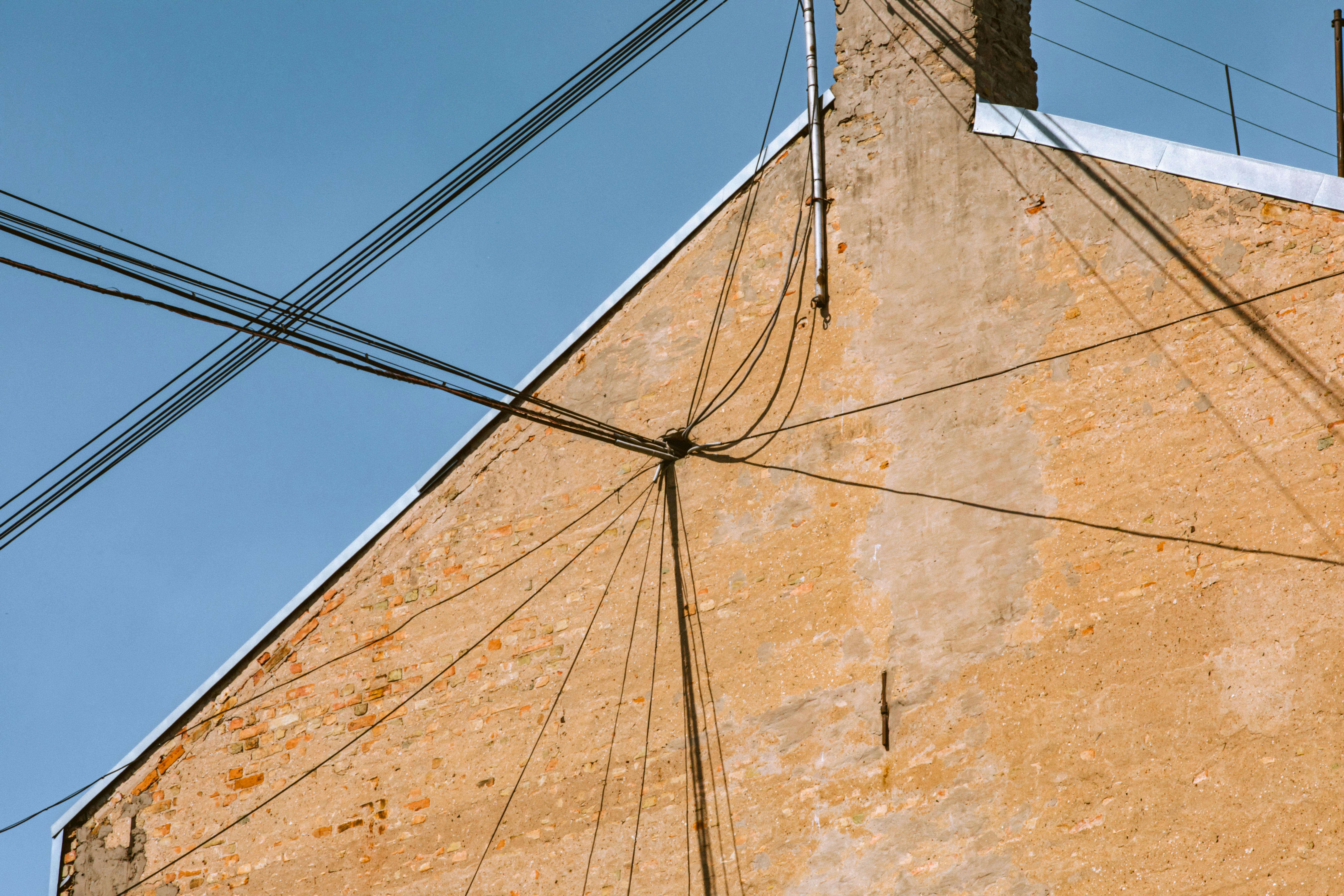 Convergence on the Facade: A web of utility cables across a sunlit brick wall