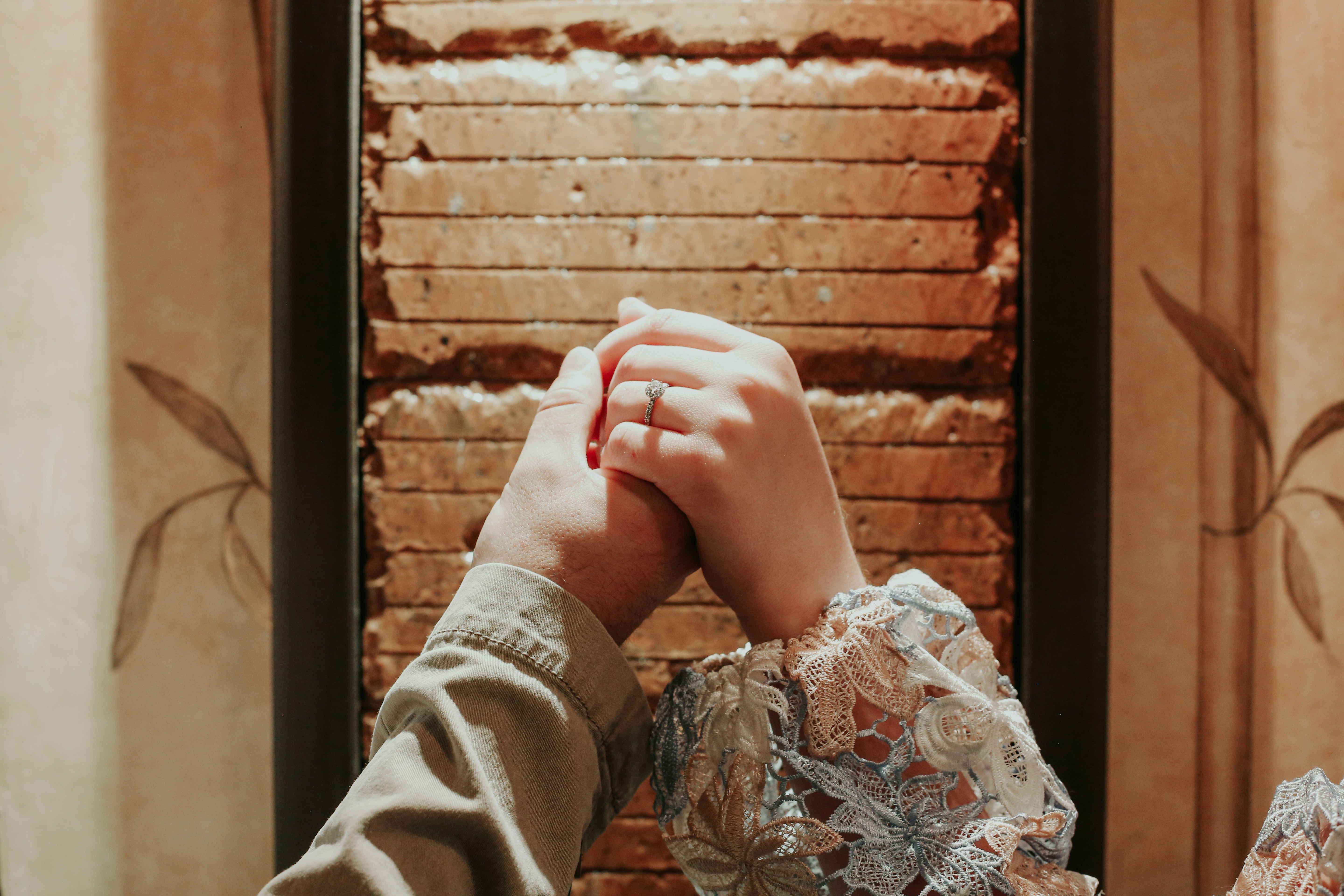 Two hands clasped together against a textured backdrop, symbolizing unity and affection. The intricate details of the lace sleeve add a touch of elegance.