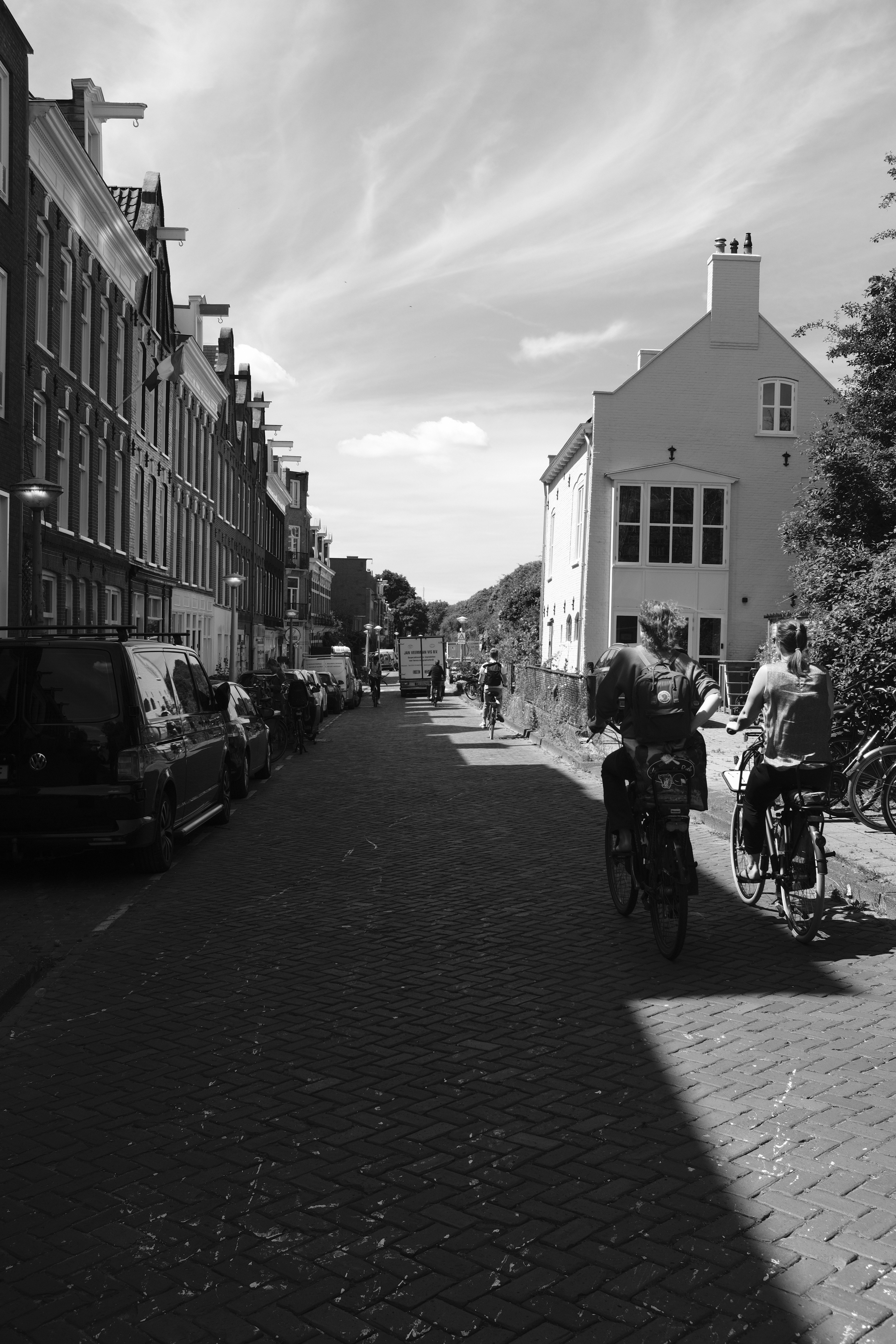 Bicyclists navigating a cobblestone street lined with charming buildings on a sunny day. The scene captures the essence of urban life and movement.