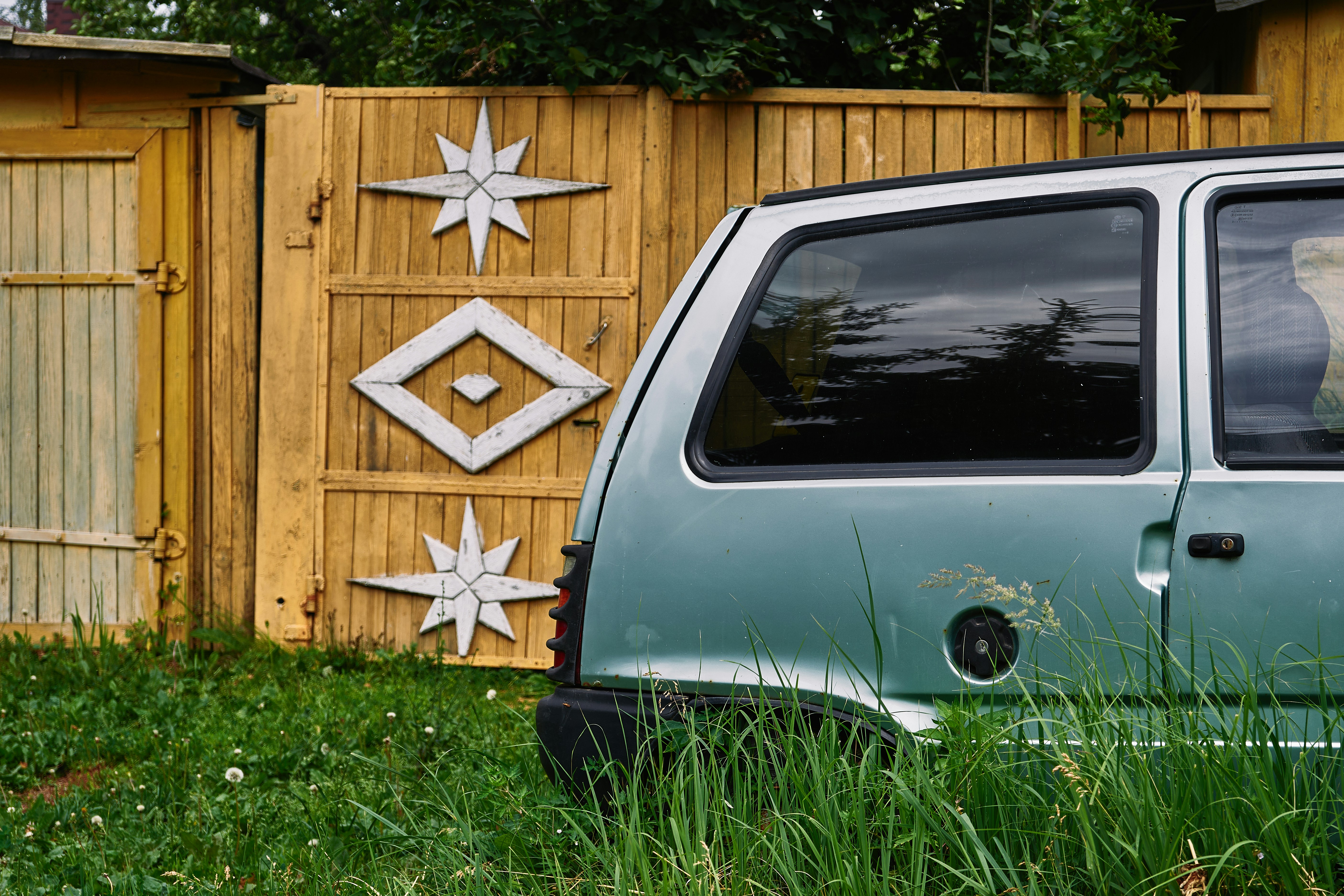 Partial VW Window Forward: A Weathered Green Vehicle Hides by a Wooden Fence