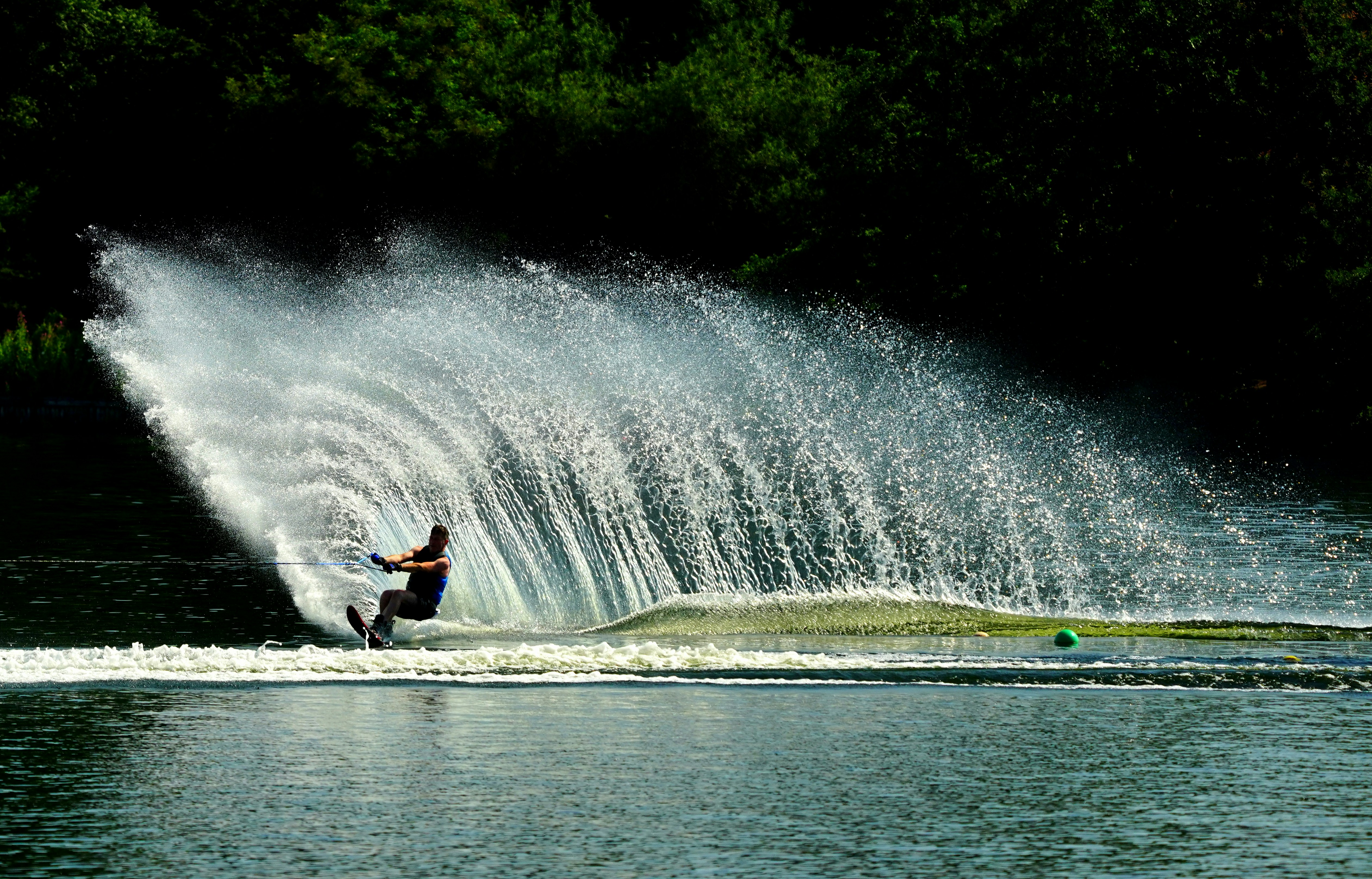 Water skier carving through the lake, creating a dramatic spray of water droplets against a serene backdrop of greenery.