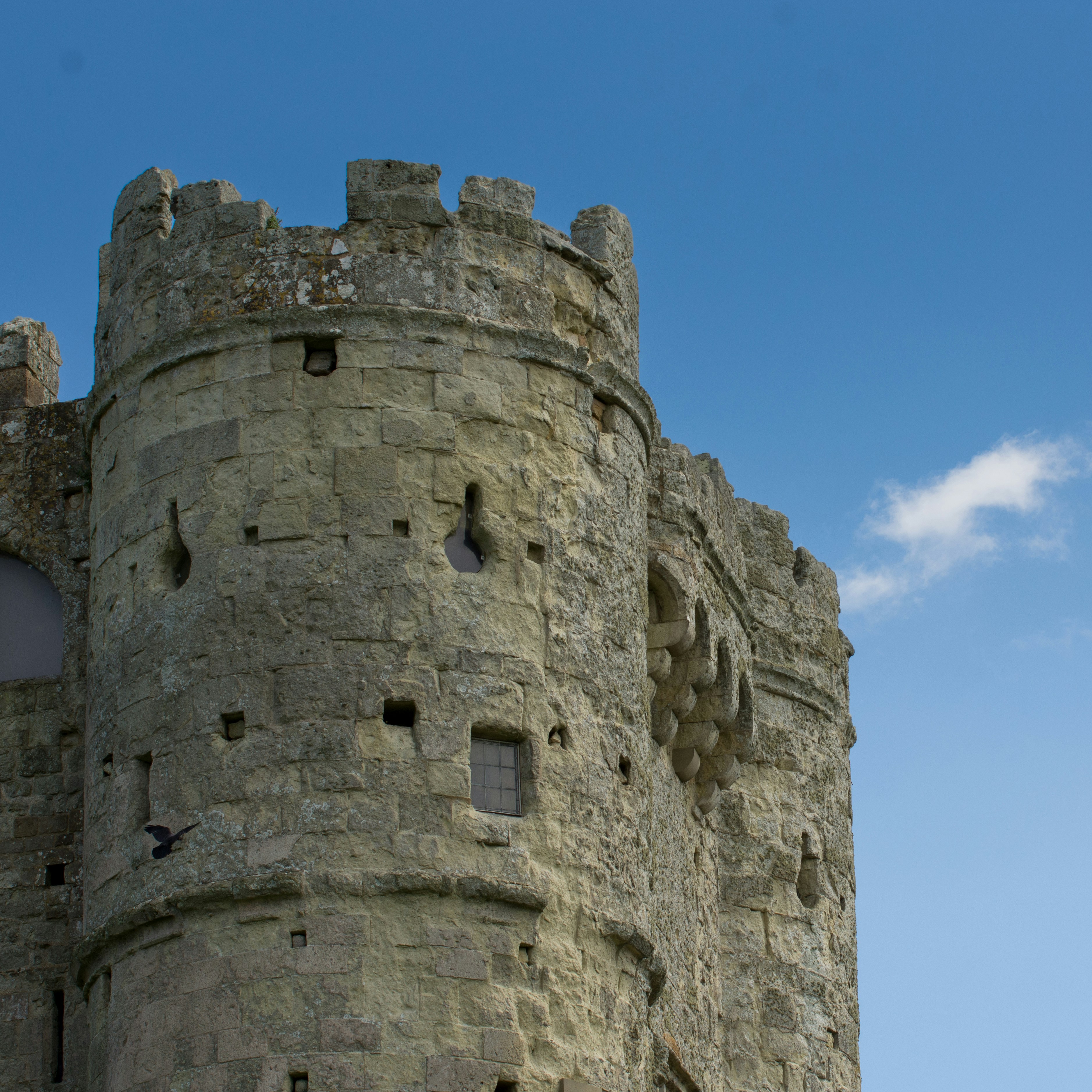 Ancient stone castle tower standing against a clear blue sky, showcasing weathered textures and architectural details.