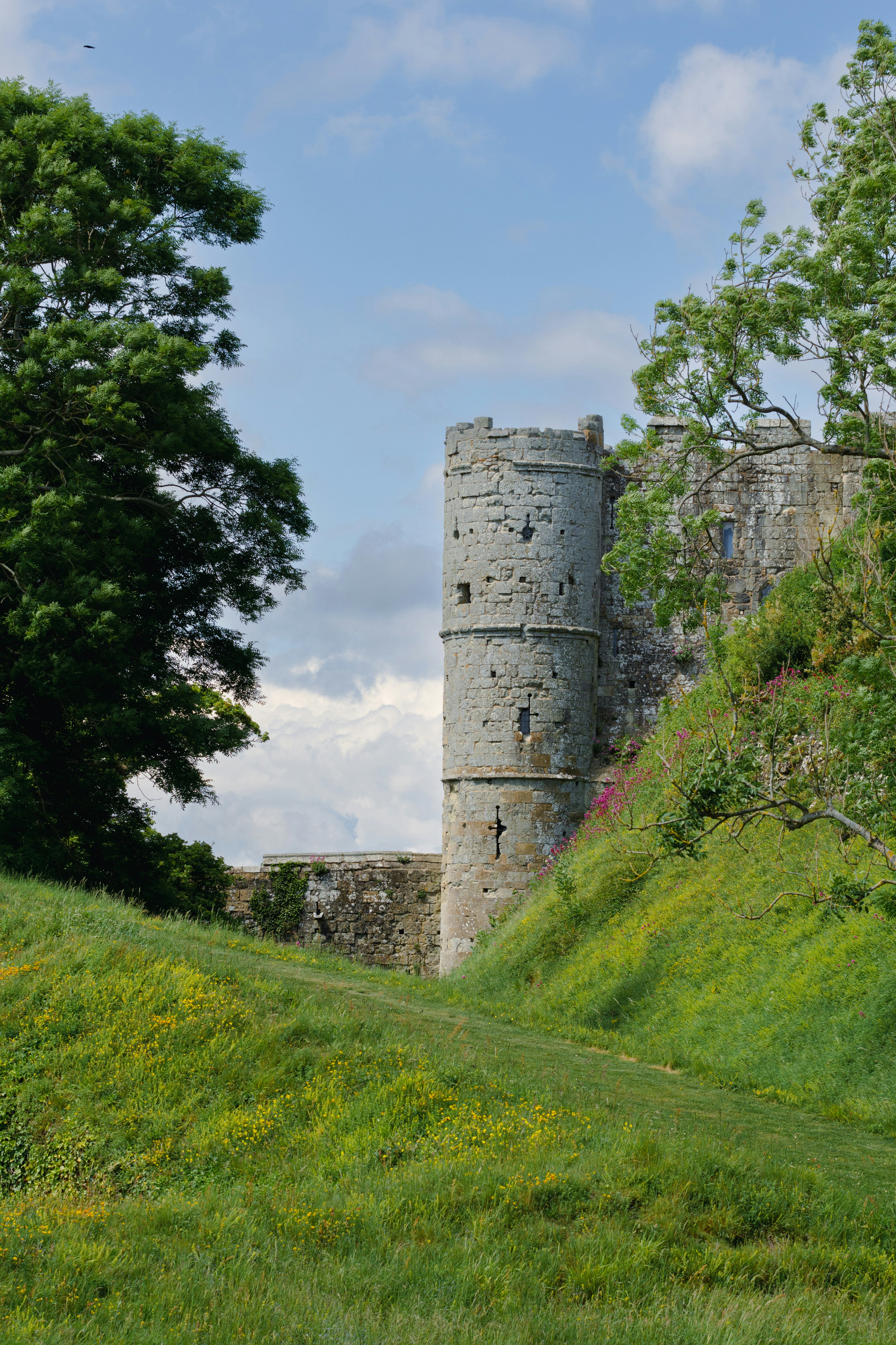 Ancient stone tower partially obscured by lush greenery, standing guard over rolling hills under a blue sky.