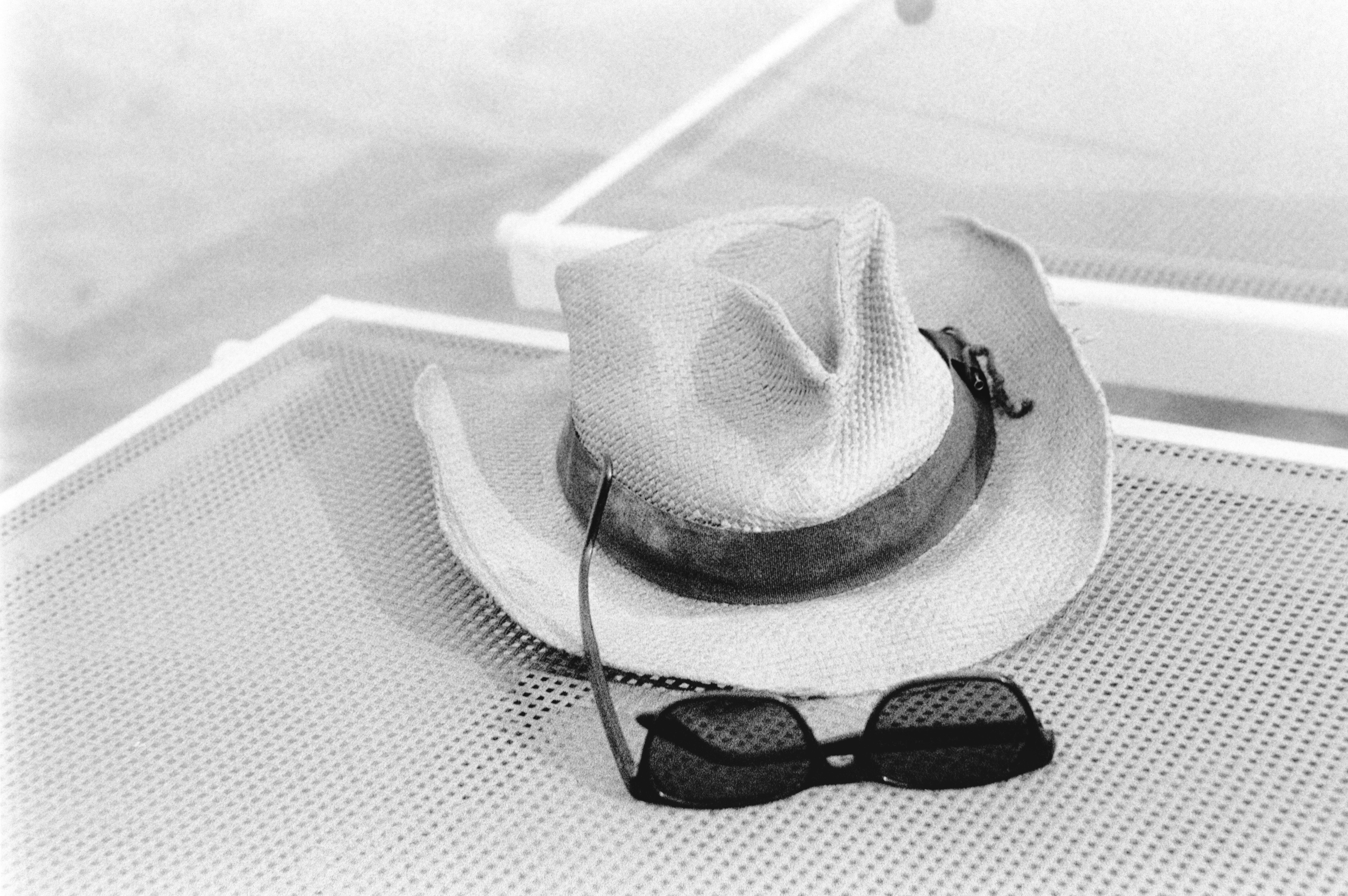 A straw hat rests beside a pair of dark sunglasses on a textured surface, evoking a sense of relaxed leisure. 