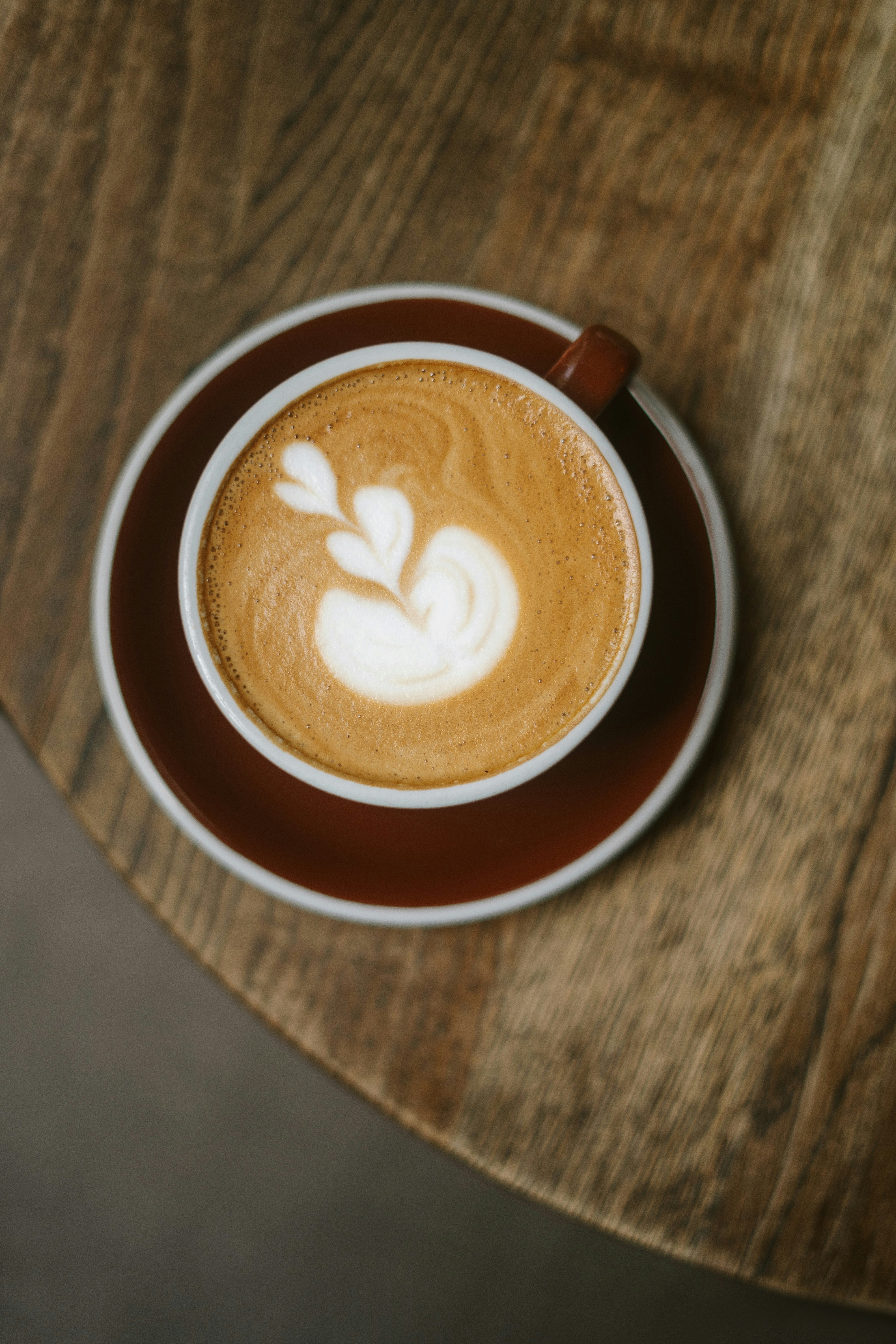 A beautifully crafted latte with intricate foam art sits atop a wooden table, inviting warmth and comfort.