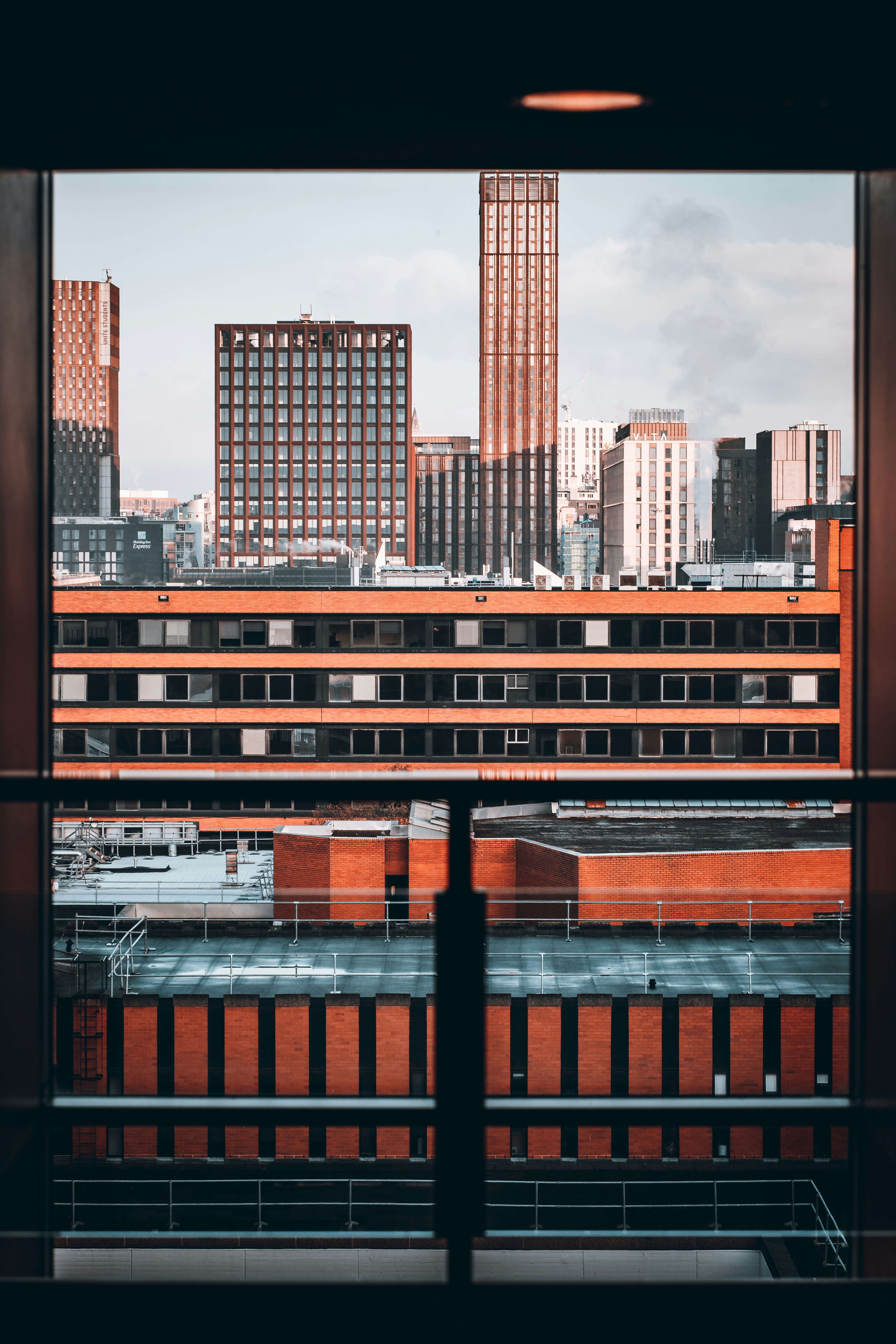 View of a modern city skyline captured through a structured window frame, showcasing contrasting architectural styles and colors.