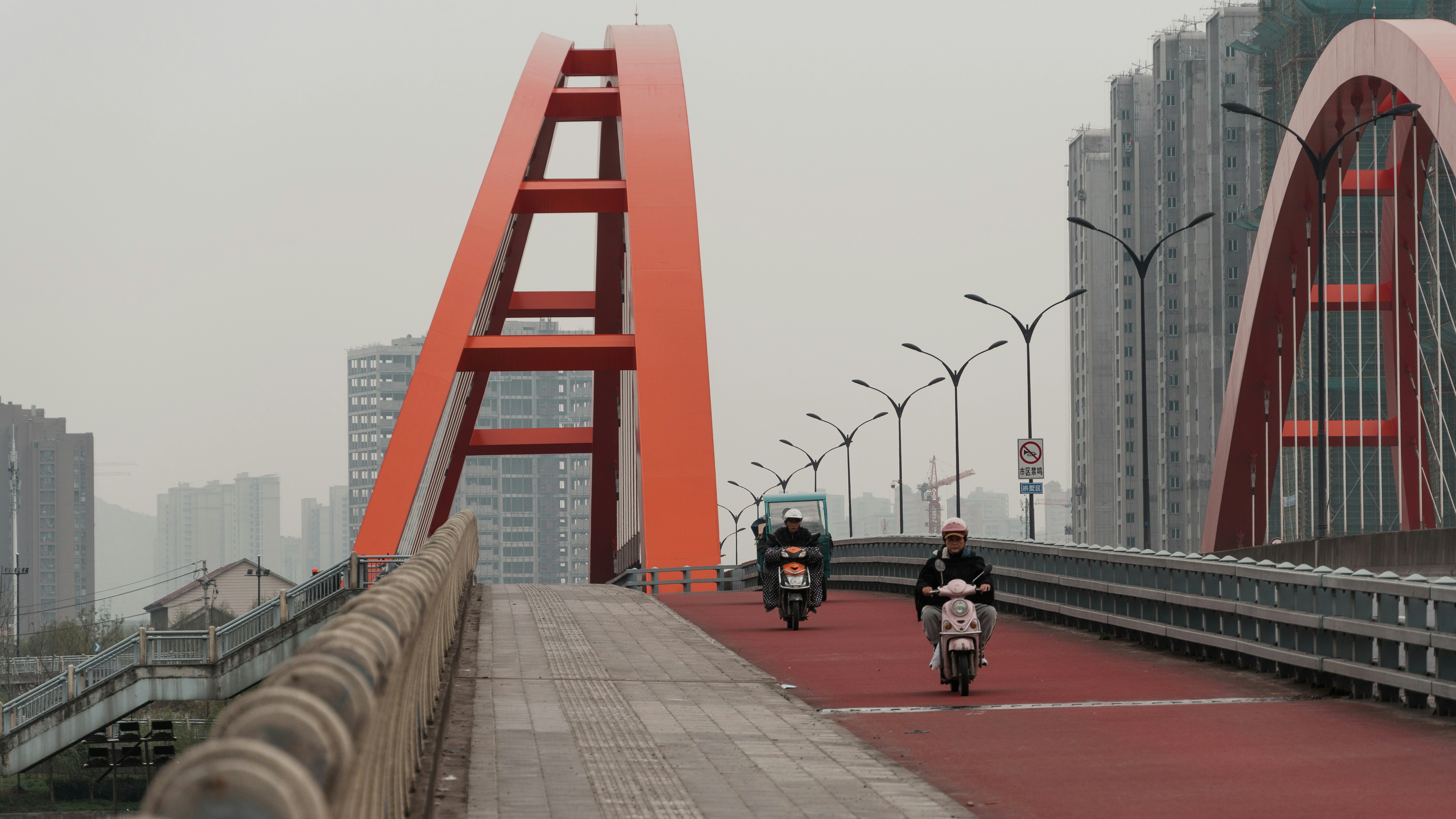 Crimson Arch Overpass: Two Riders Glide Across a Quiet City Bridge