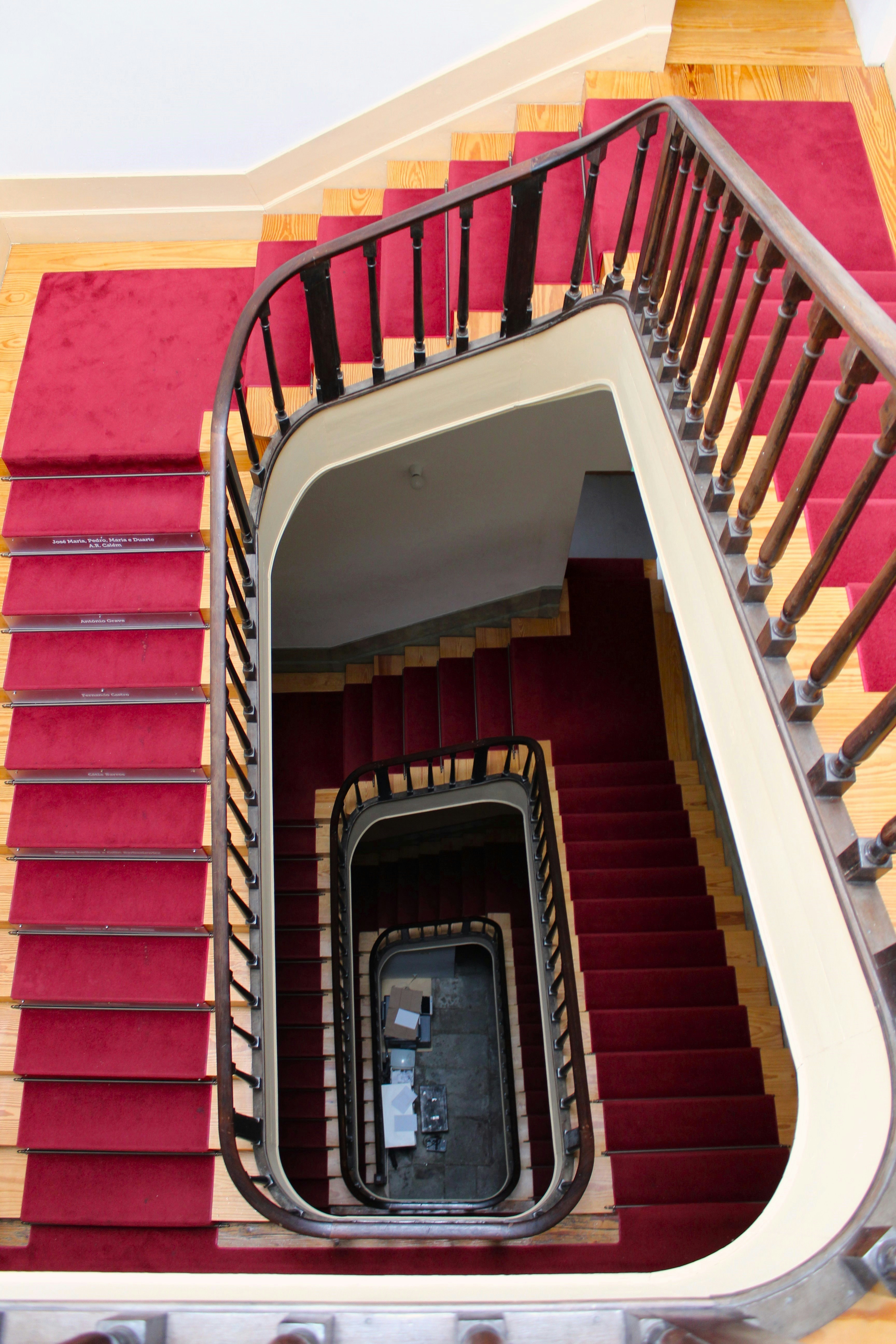 Spiral staircase with red carpet and ornate railing viewed from above.