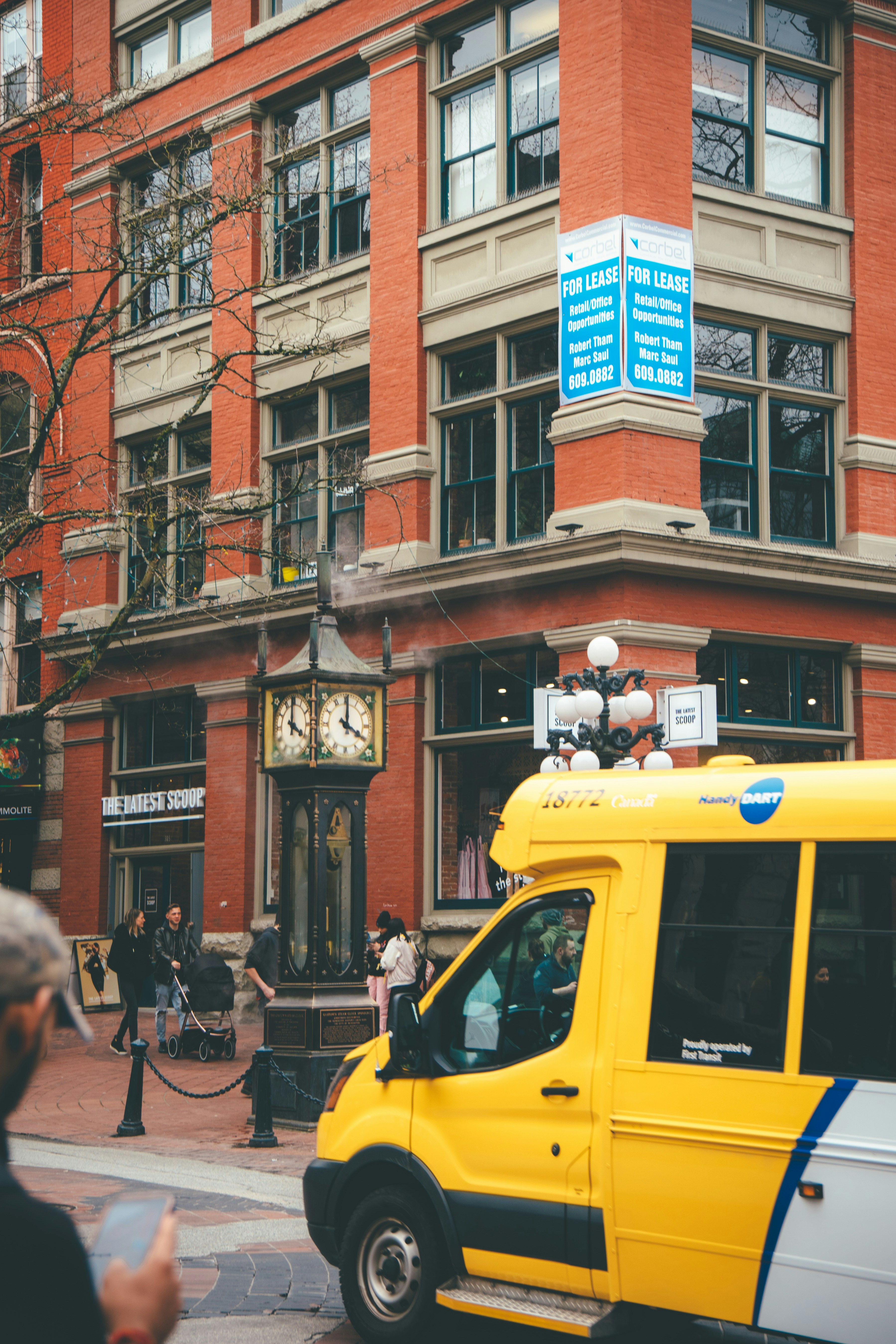 Yellow van at a brick urban corner with a street clock and storefronts