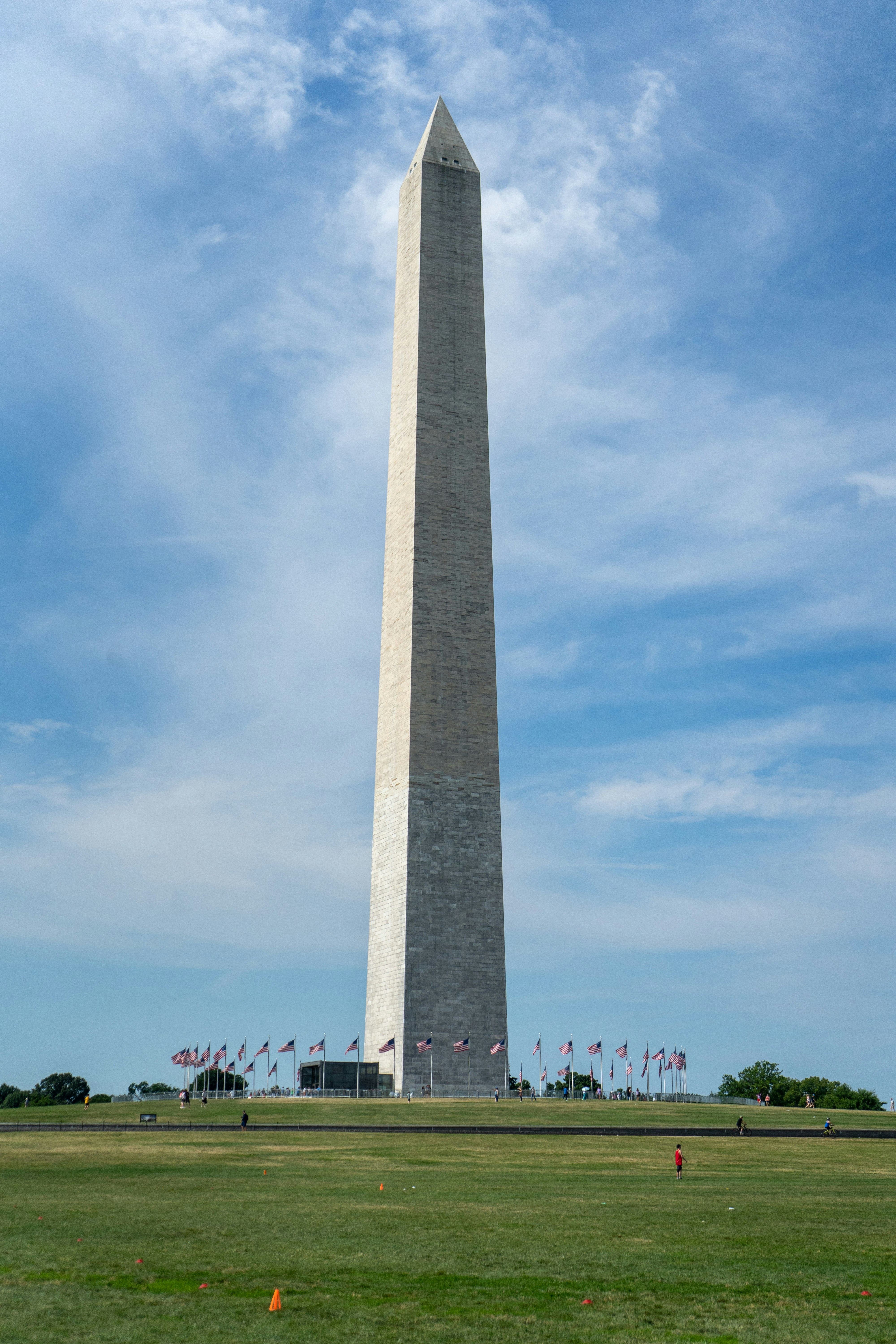 Washington Monument standing tall against a clear blue sky, surrounded by flags and green lawn. A symbol of American history and resilience.