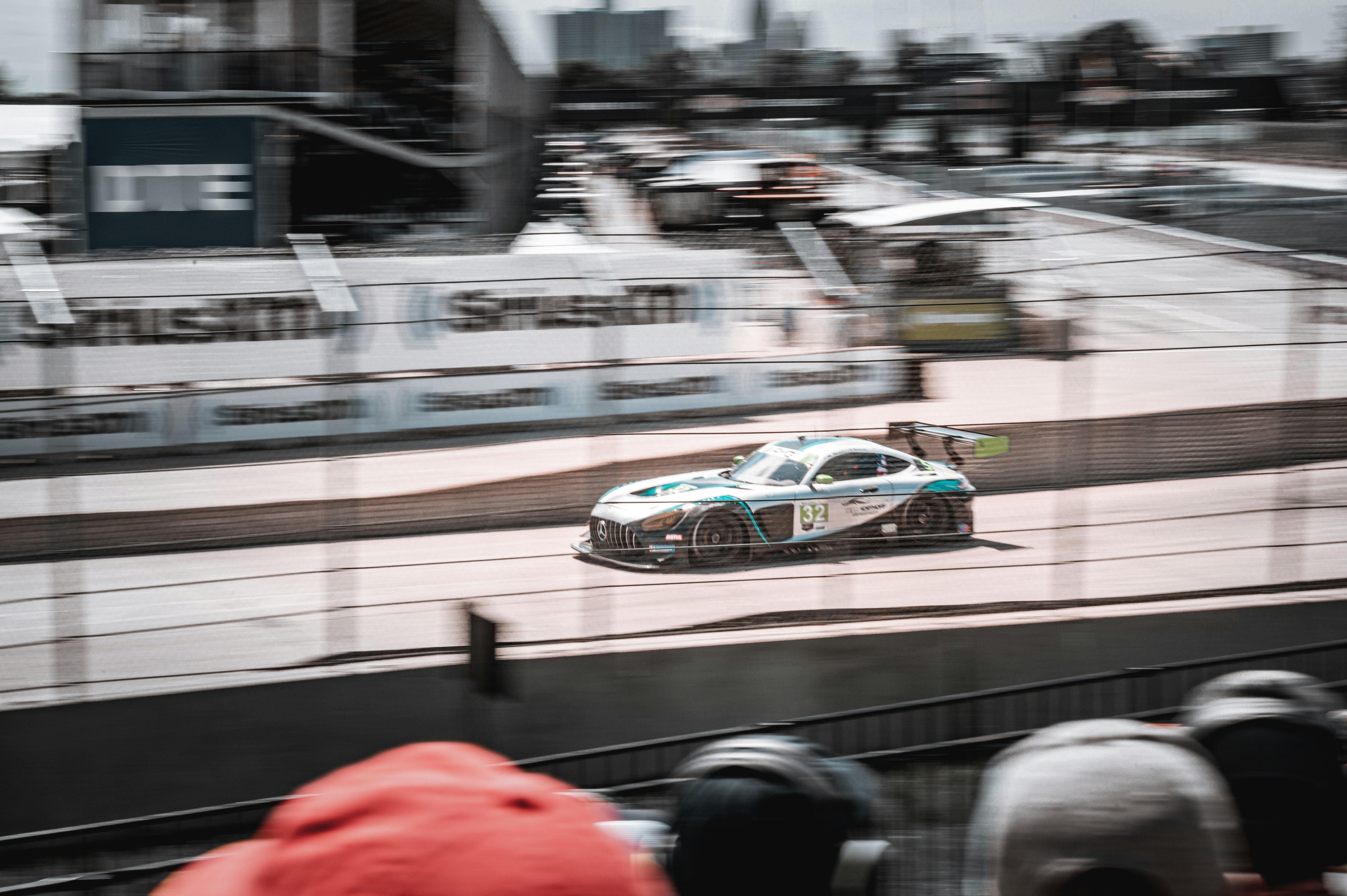 A sleek racing car speeds around a track, captured in a dynamic blur that conveys motion and excitement. The backdrop features spectators and signage, enhancing the racing atmosphere.