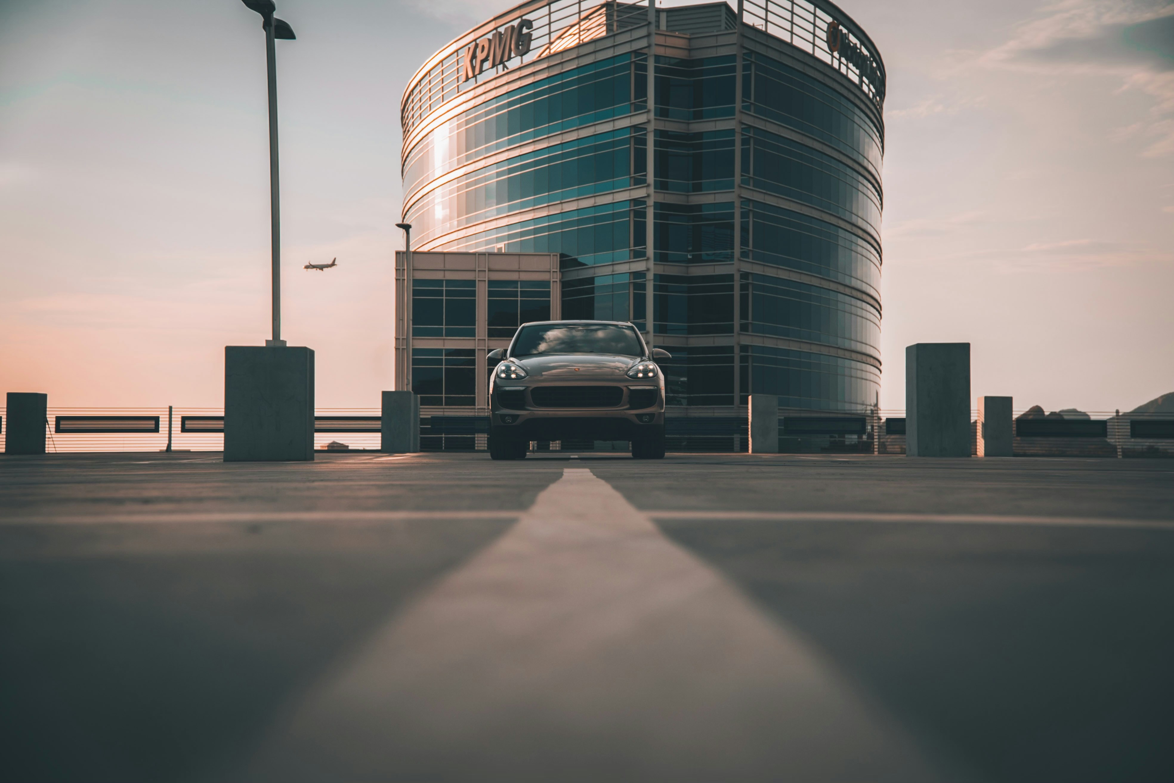 Car parked on a rooftop with a modern cylindrical building in the background at sunset.