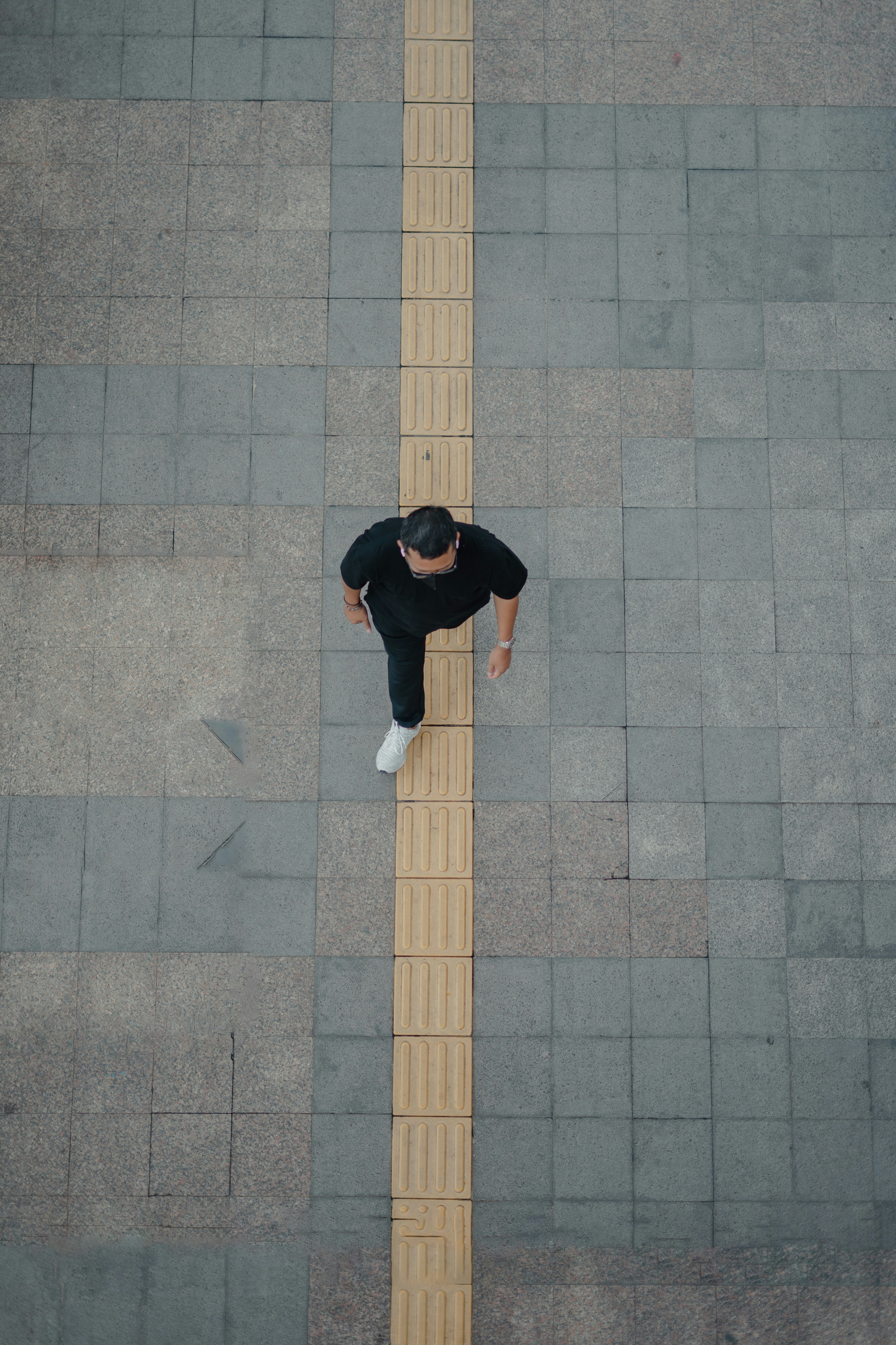 A person walking along a tactile paving path in an urban environment, emphasizing movement and direction.