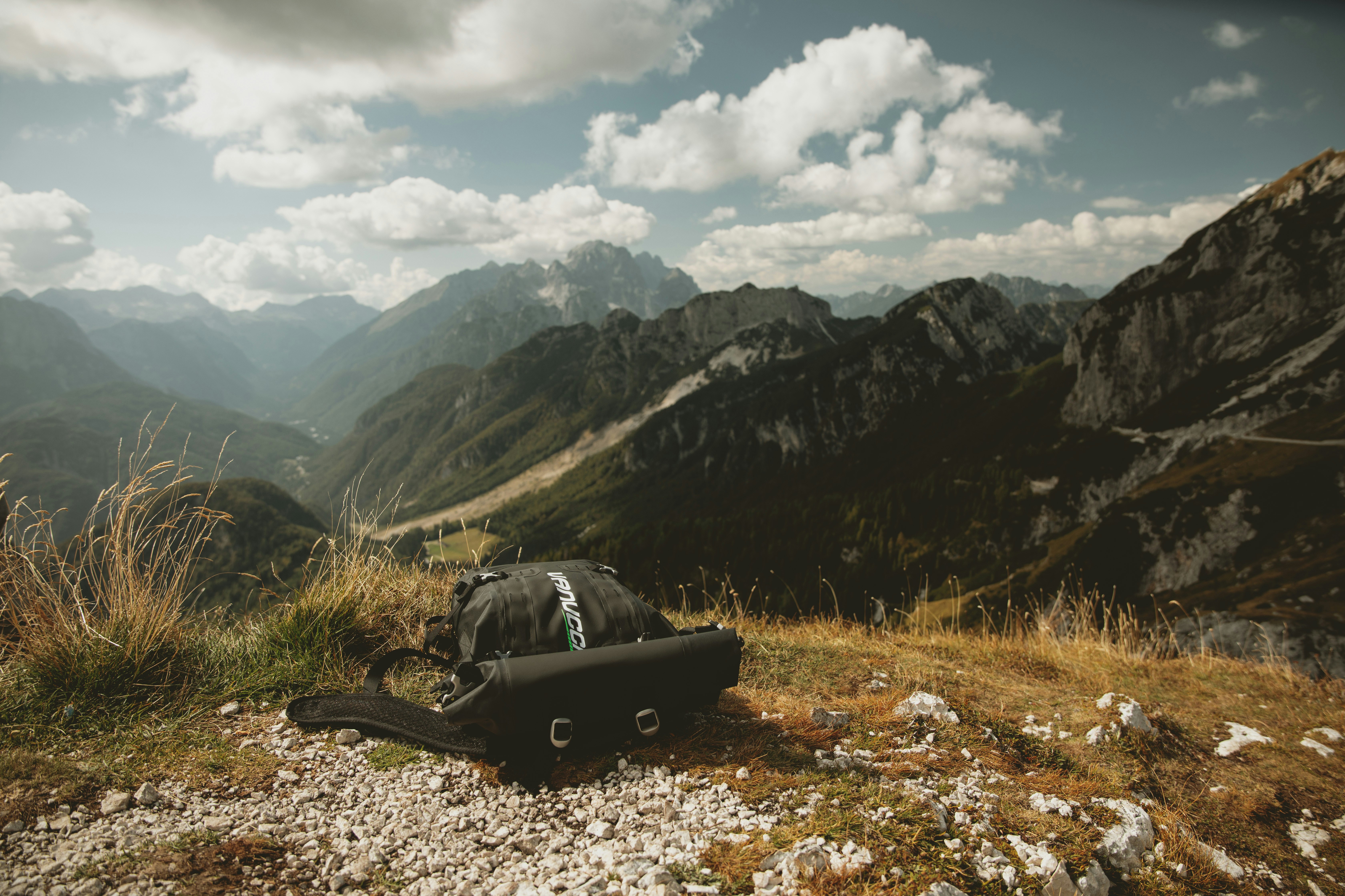 Vanucci backpack resting on a rocky ledge overlooking a sprawling mountain valley under a partly cloudy sky.