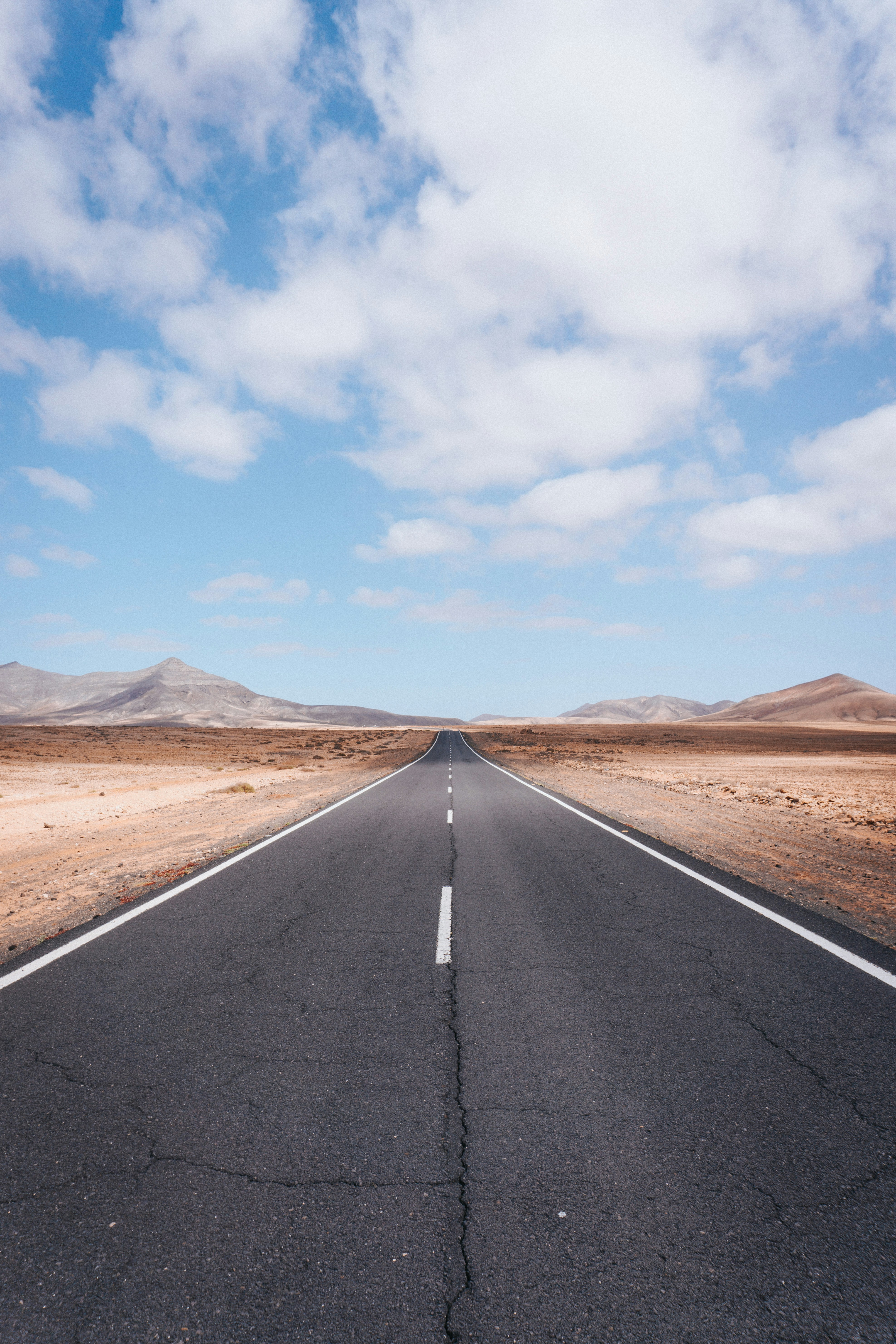 Long, straight road stretching through a barren landscape under a partly cloudy sky.