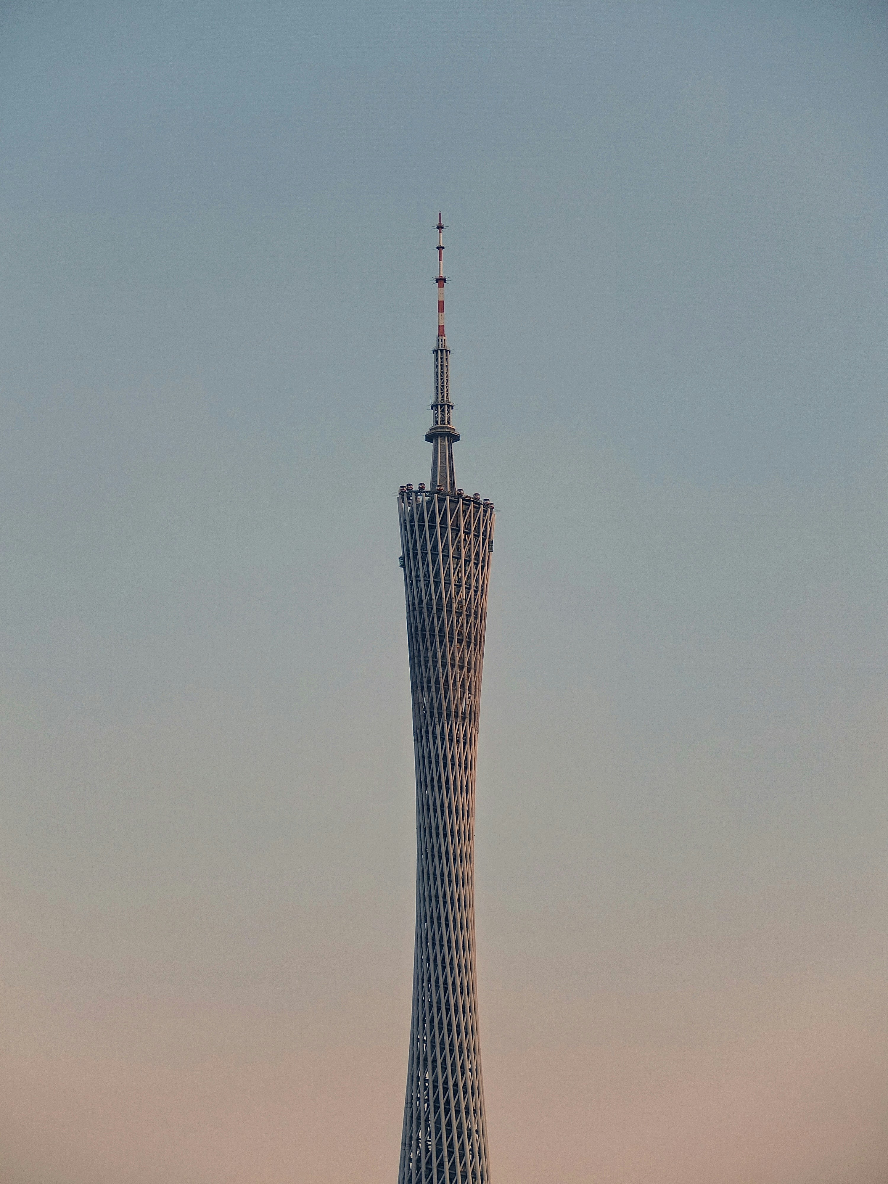 Towering structure with a sleek, twisting design against a pastel sky. The pinnacle features red and white accents.