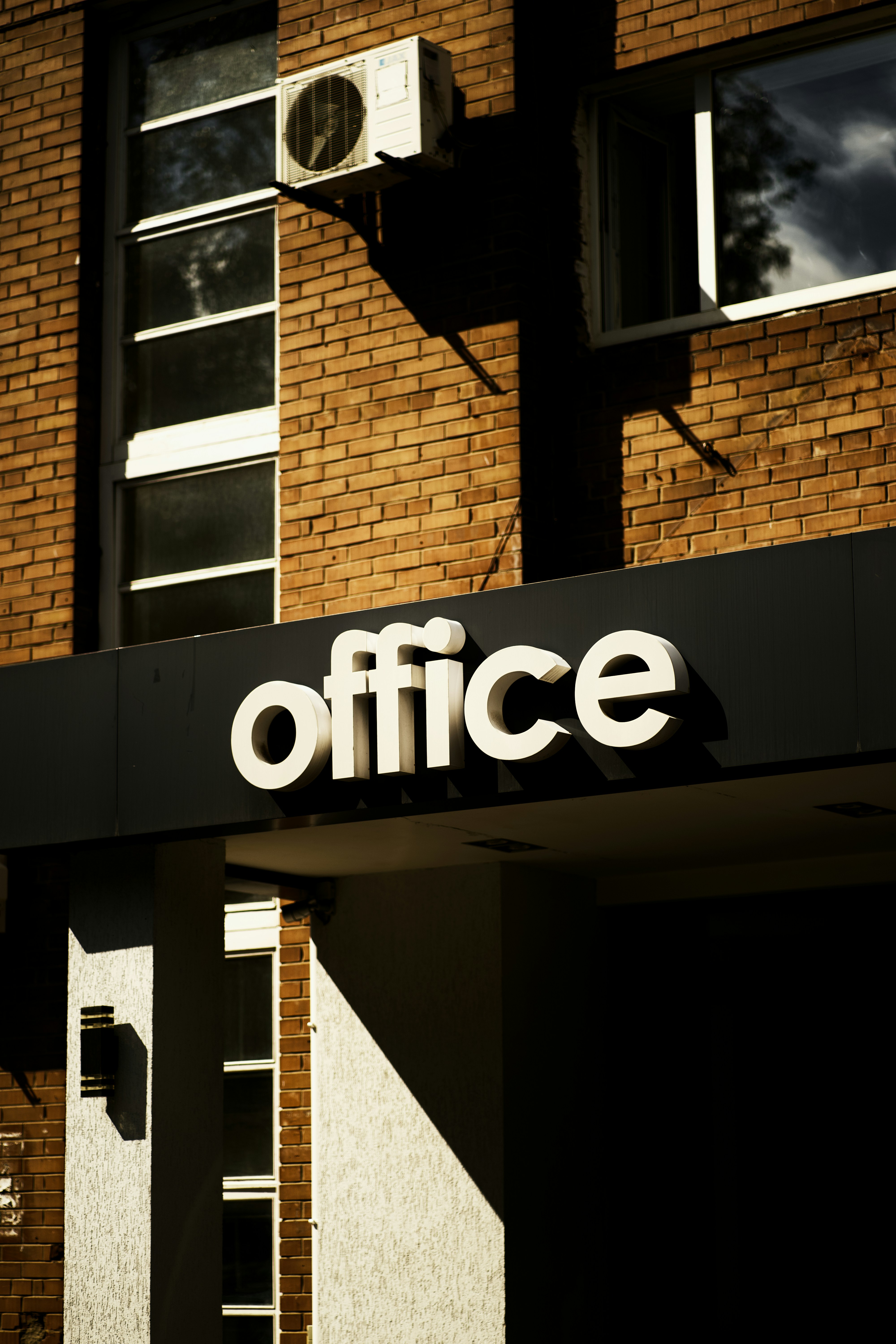 Sunlit Brick Facade: The Bold Office Sign and Shadowed Entrance