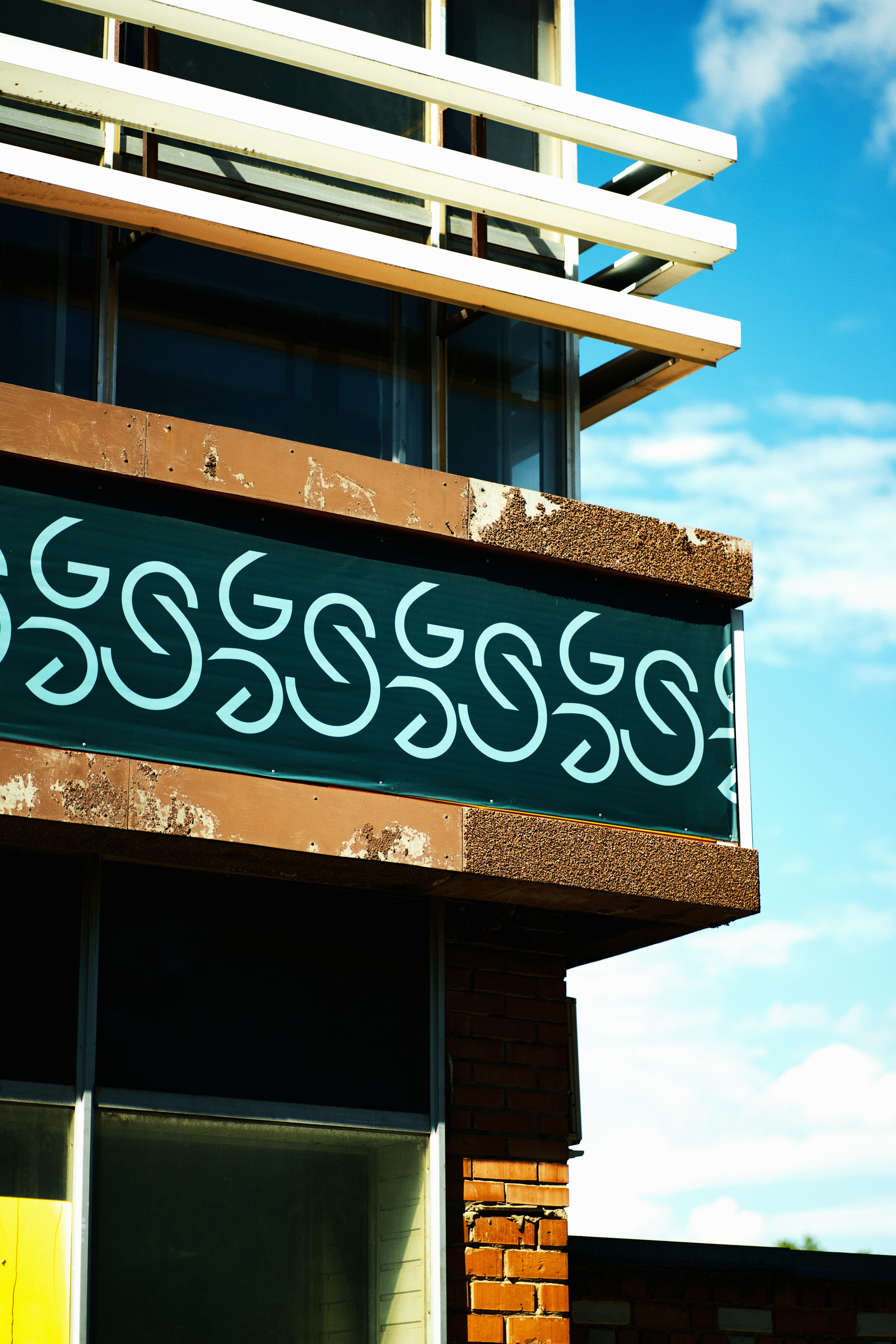 Teal S-pattern Sign Clinging to a Rusted Facade Under a Bright Blue Sky